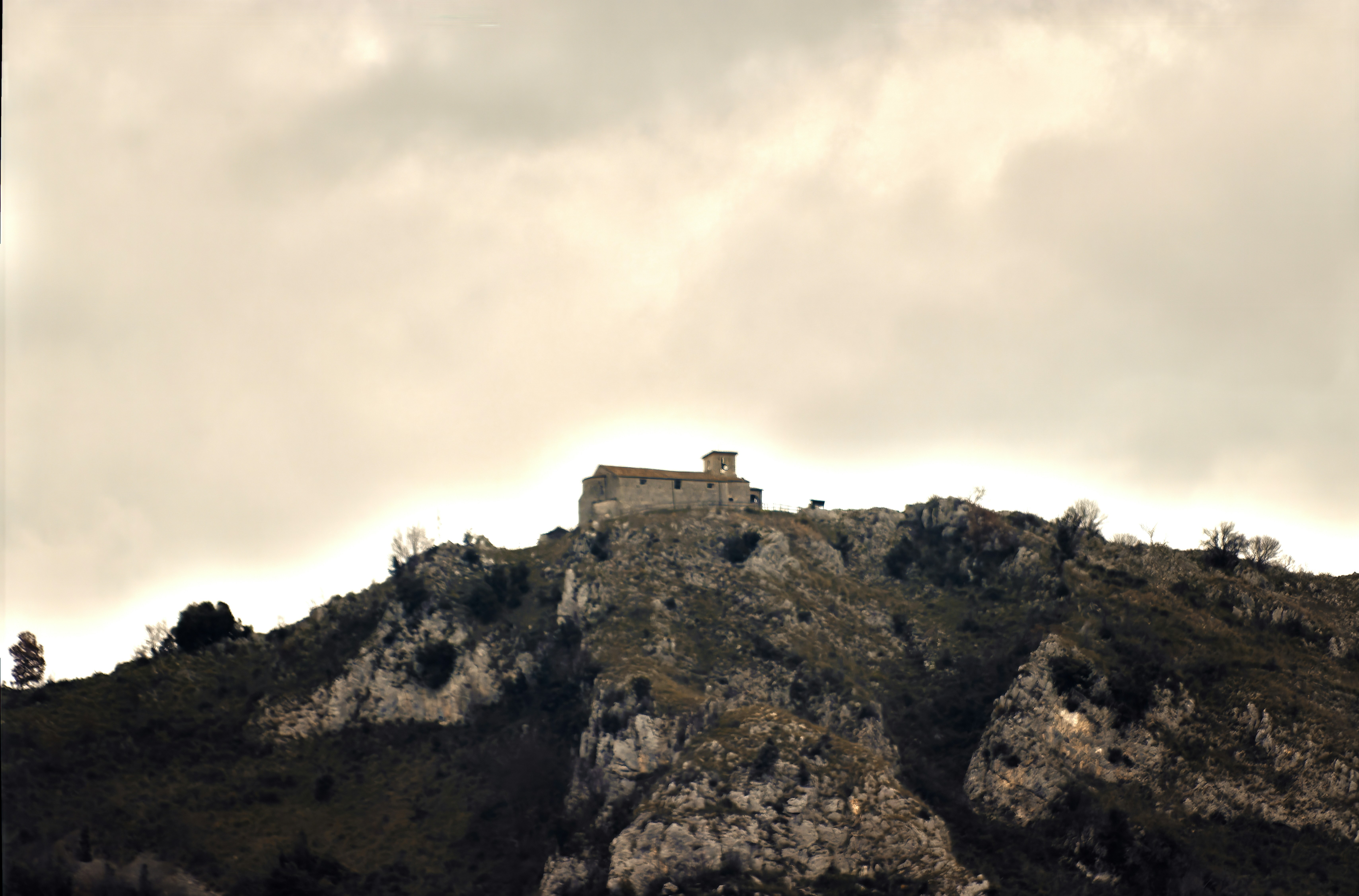 Ancient fortress perched on a rugged, rocky mountain under a cloudy sky.
