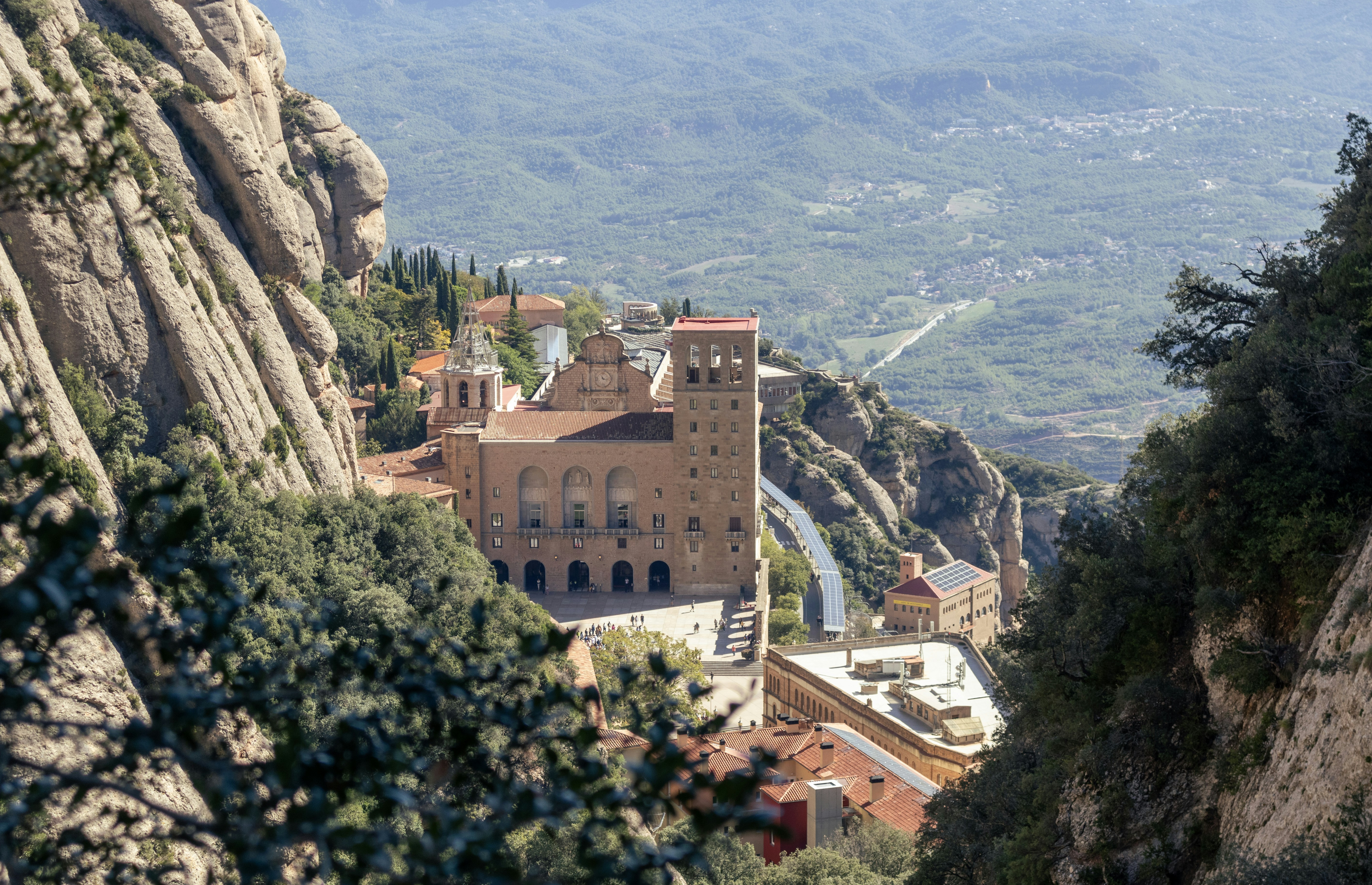 Monastery nestled within rugged mountain cliffs under a vast, lush landscape.