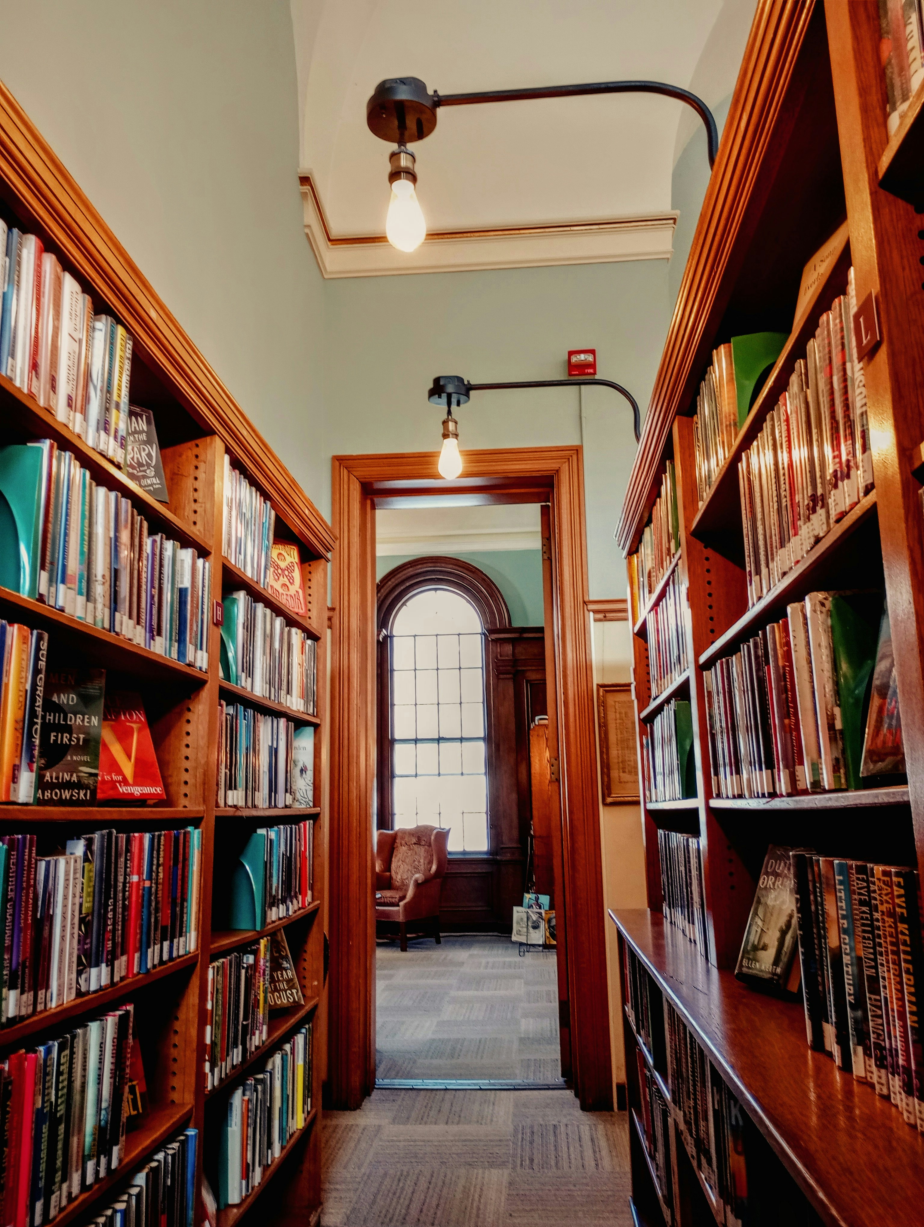 Bookshelves lined with colorful spines lead to a cozy reading nook bathed in warm light. The inviting hallway hints at a tranquil escape into literature.