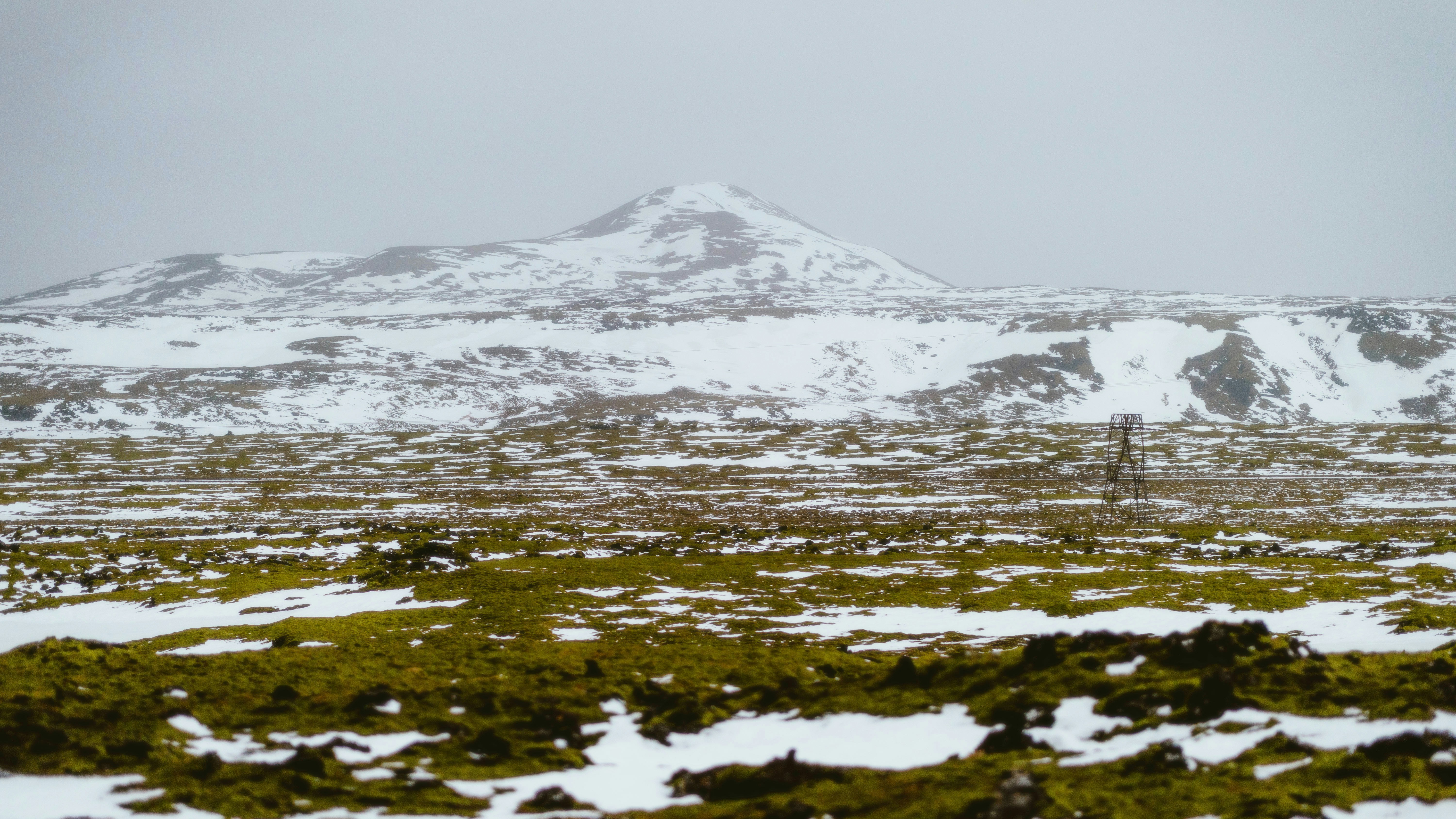 Snowy mountain landscape with sparse green patches and a solitary metal structure.