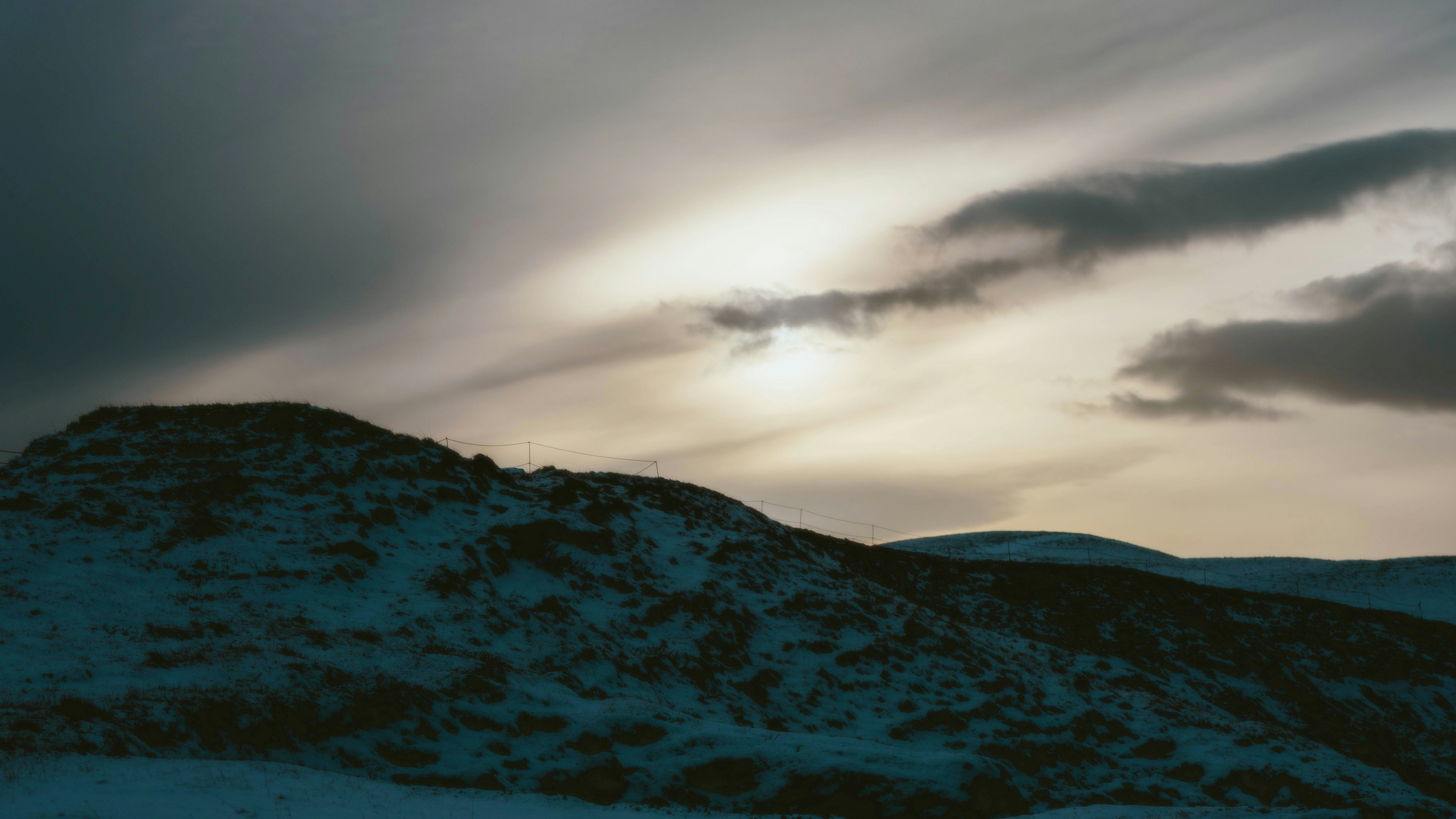 Dark hills silhouetted against a cloudy sky with a setting sun.