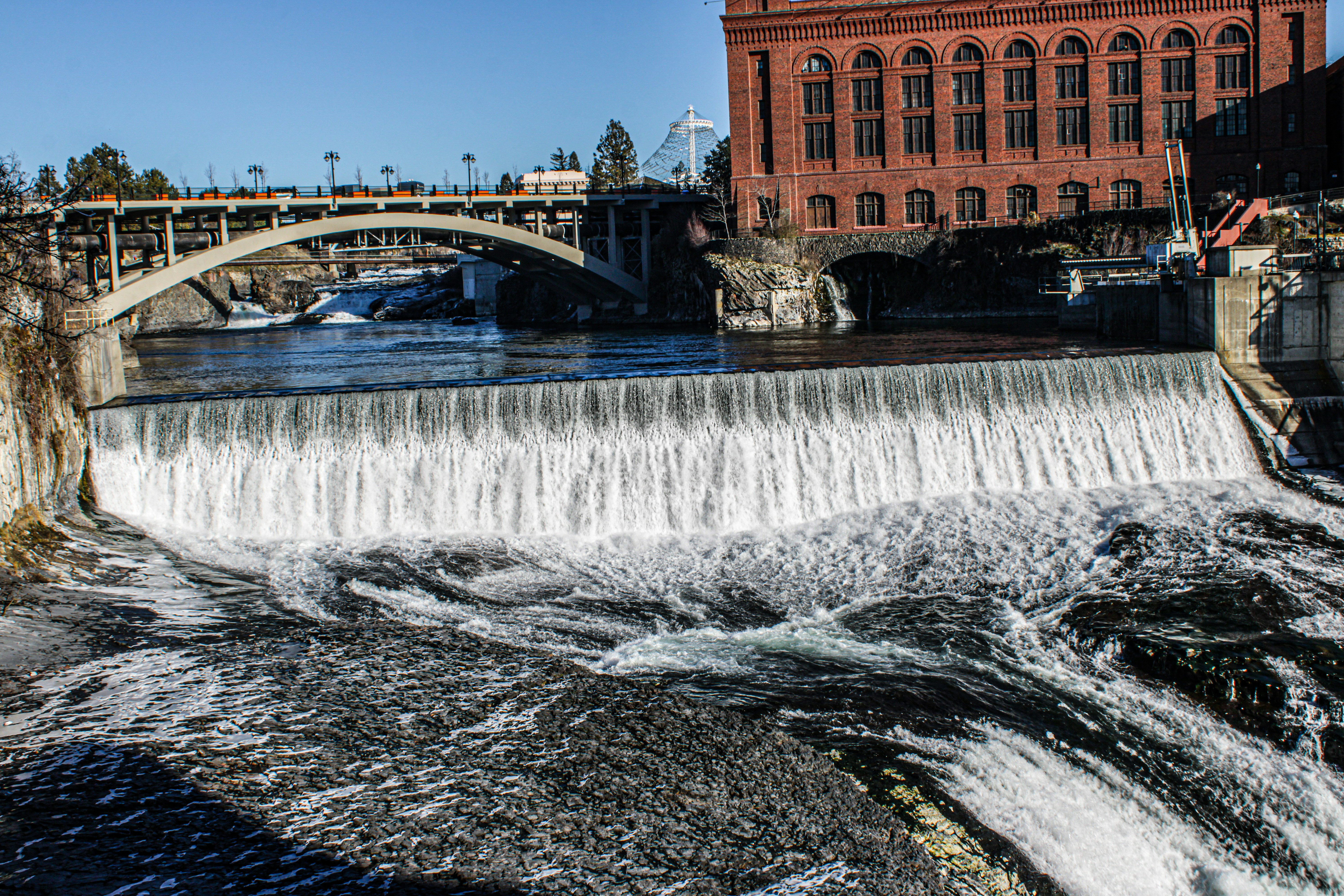 A waterfall flows under a bridge and building. photo – Free Building ...