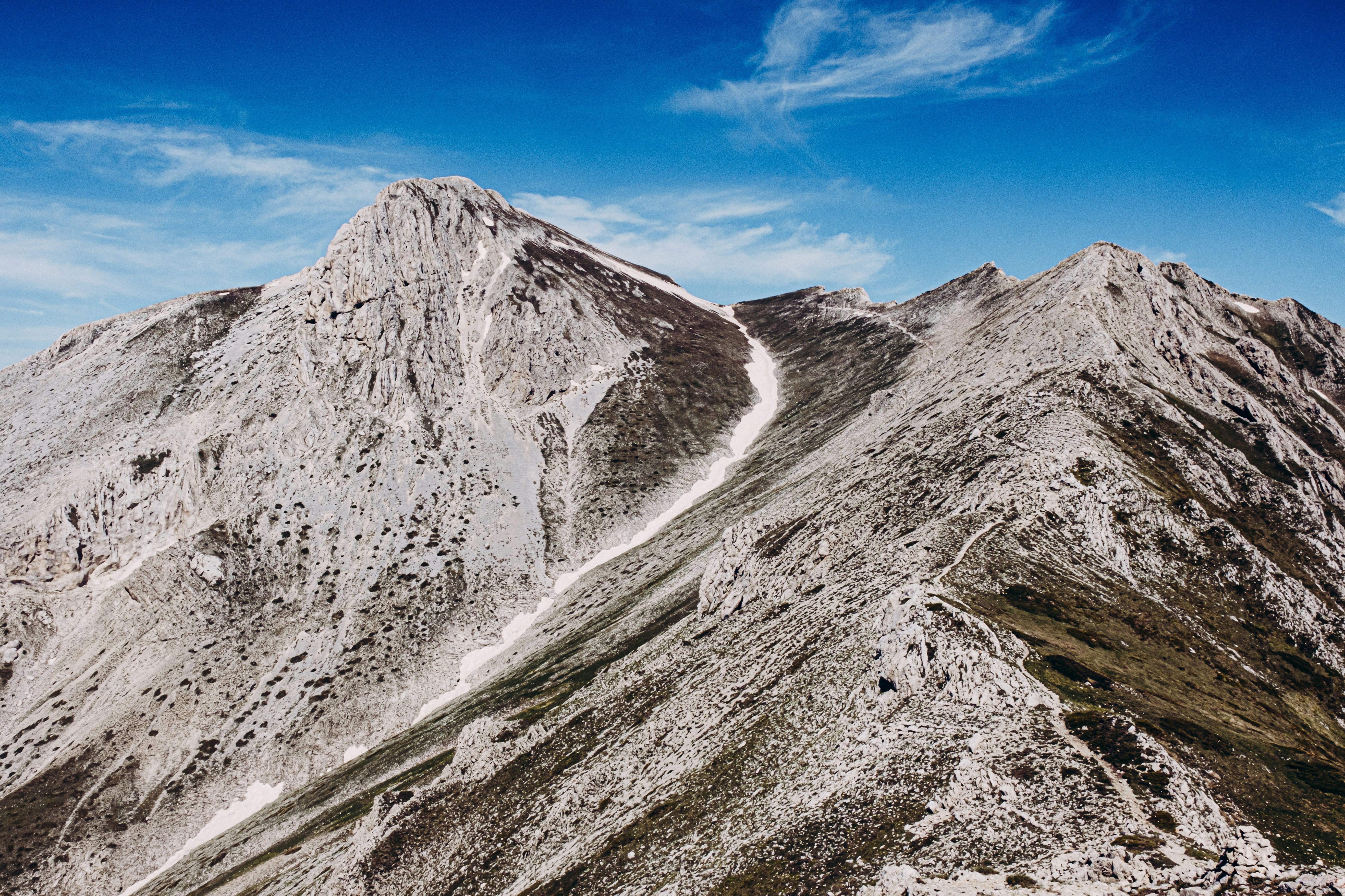 Craggy mountain peaks with a winding path beneath a bright blue sky.