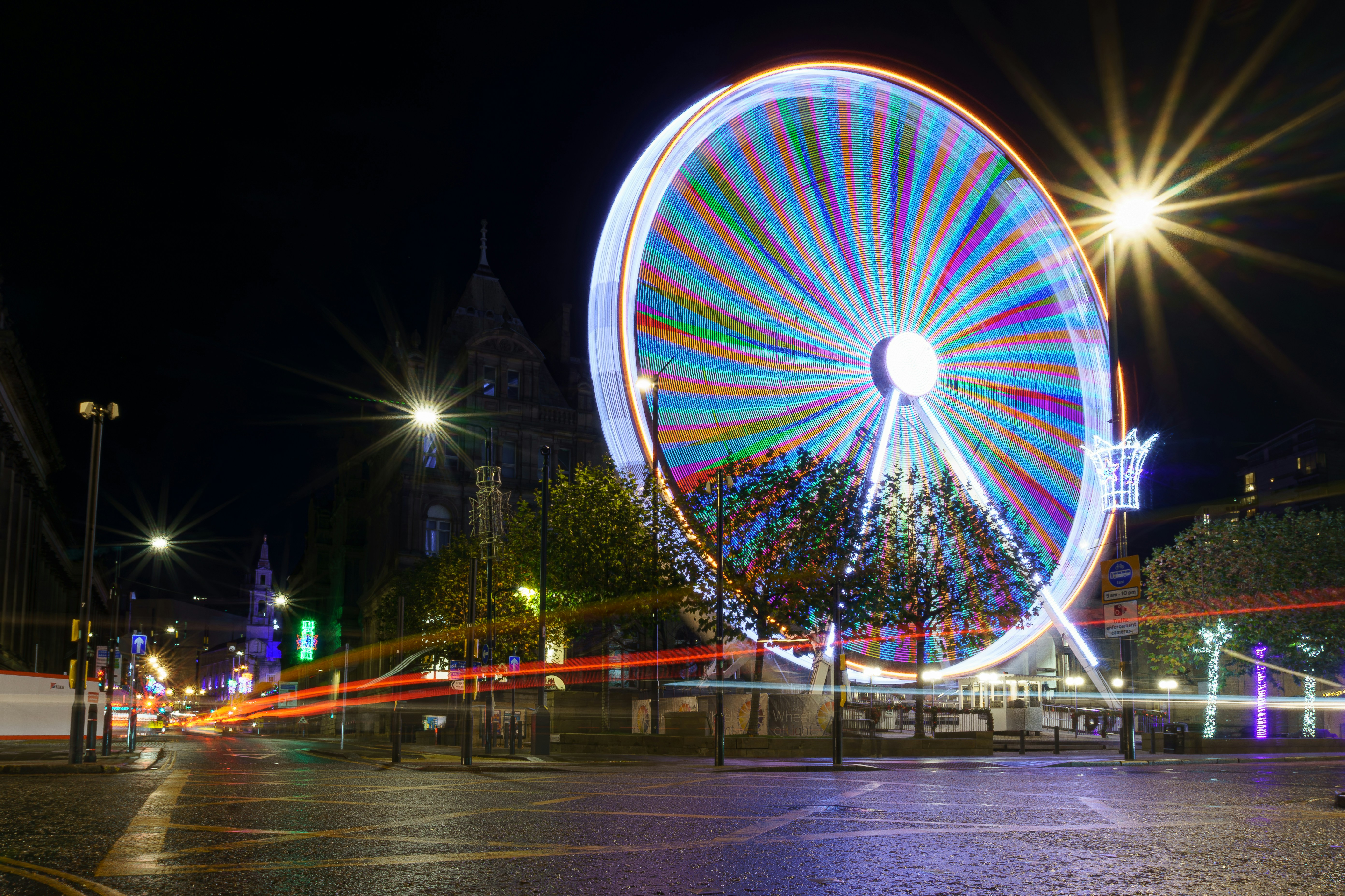 Illuminated Ferris wheel spins against a dark cityscape, creating colorful light trails.