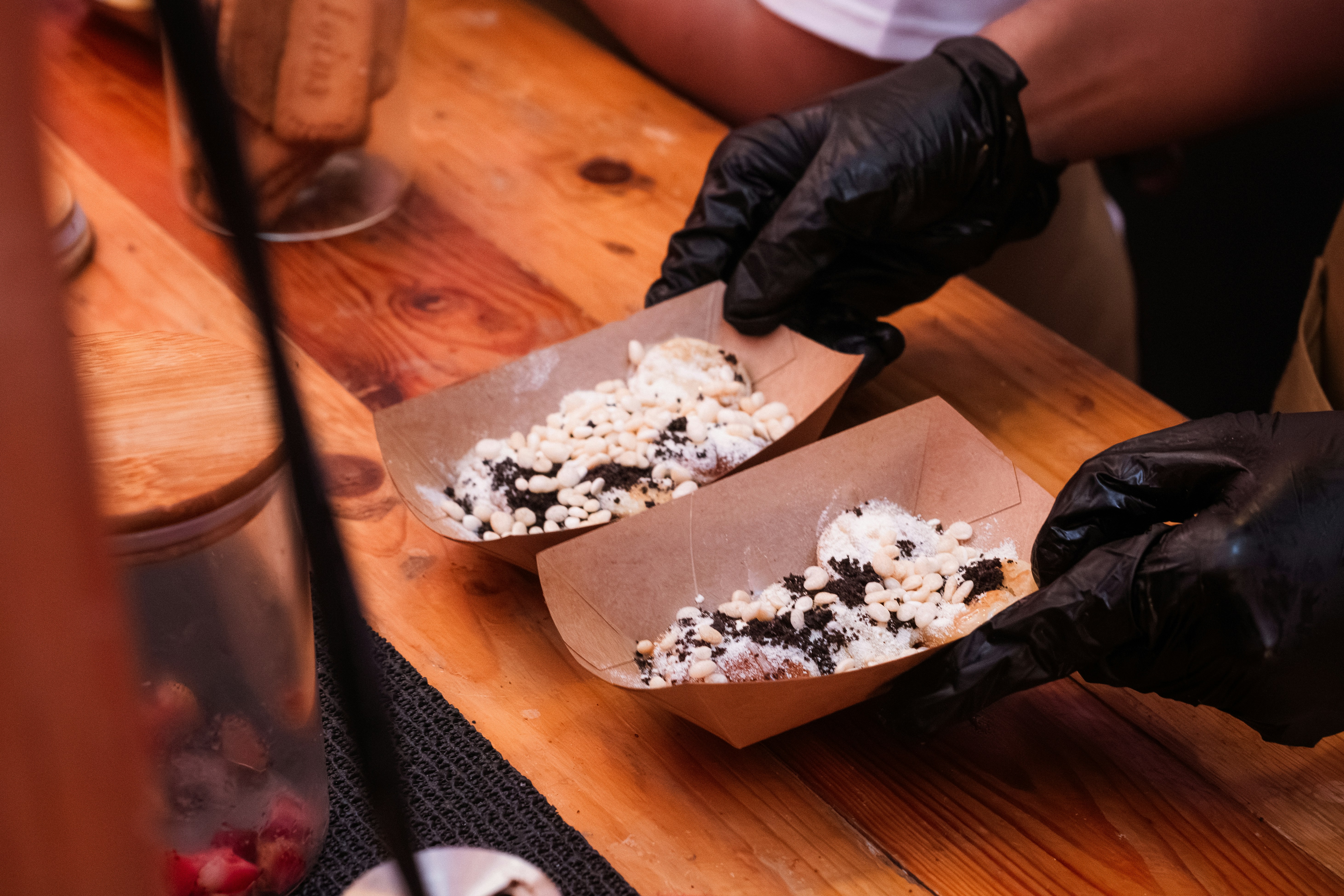 Gloved Hands Arranging Snack Bites in Paper Boats on Wood Counter