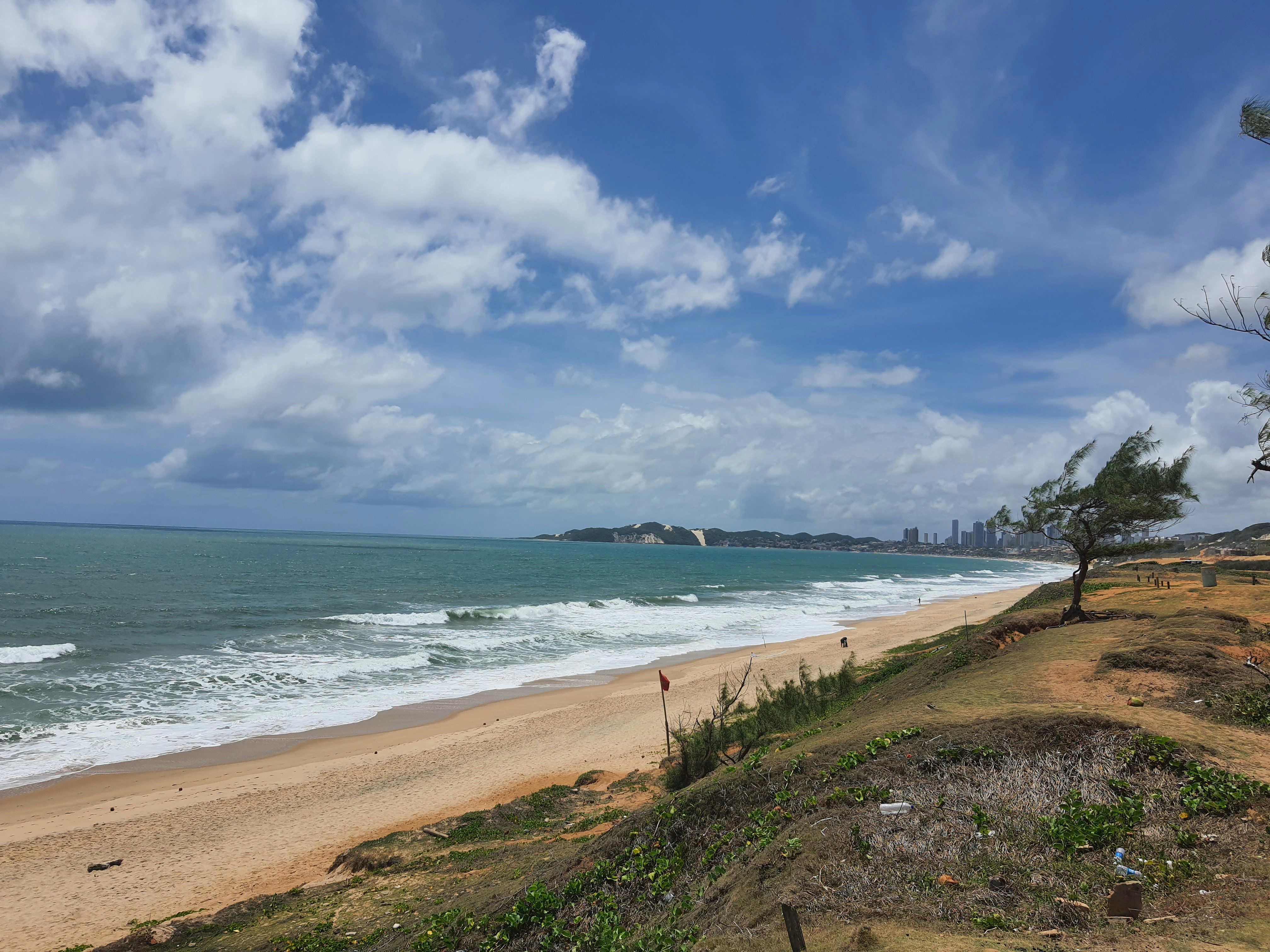 Waves gently lap against a sandy beach under a sky dotted with clouds.
