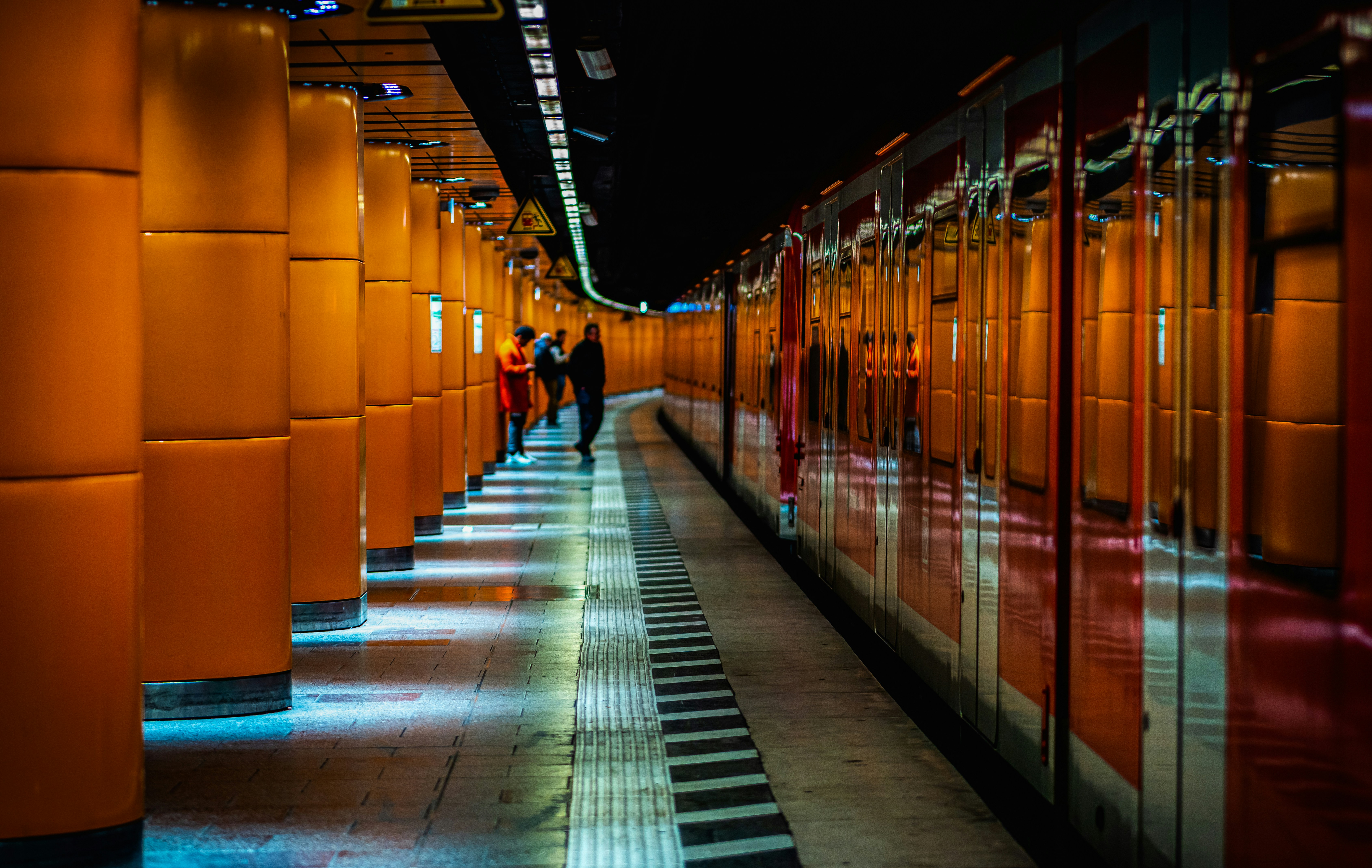 Neon Corridor at Platform Edge: Two Figures Beneath Orange Pillars