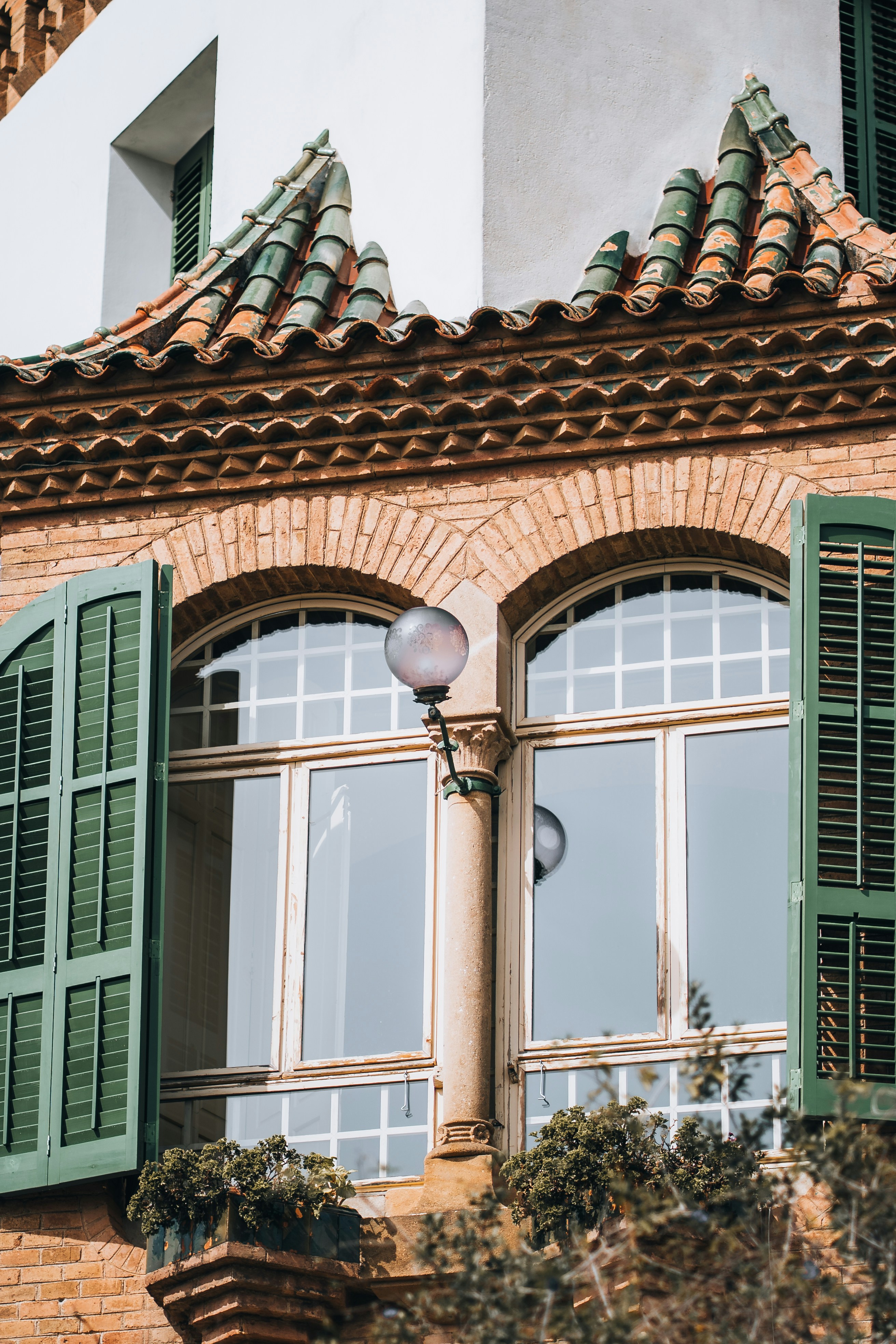 Arched windows with green shutters on a brick facade under a terracotta-tiled roof.