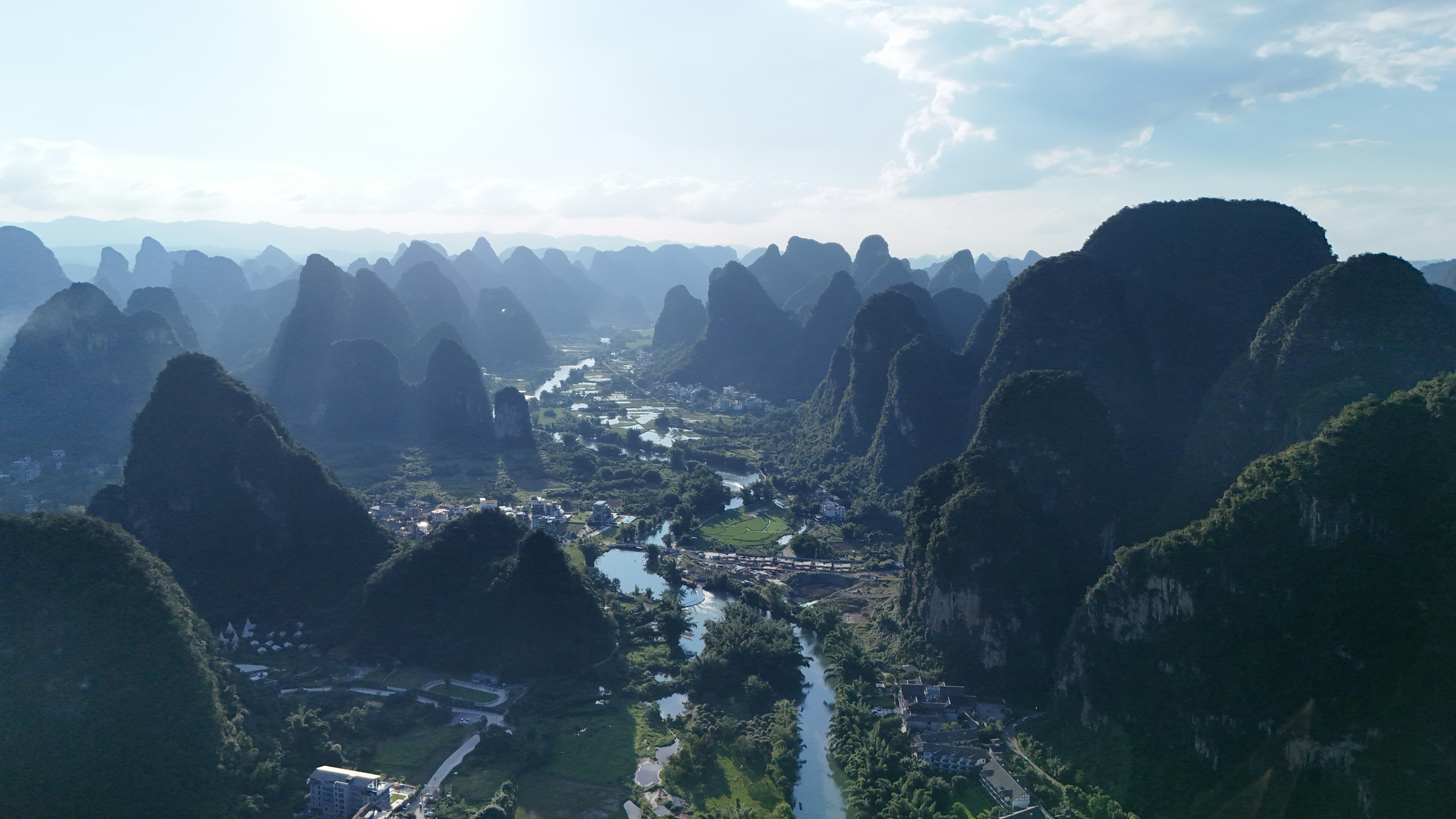 Sunlit valley with a winding river flanked by towering karst mountains.