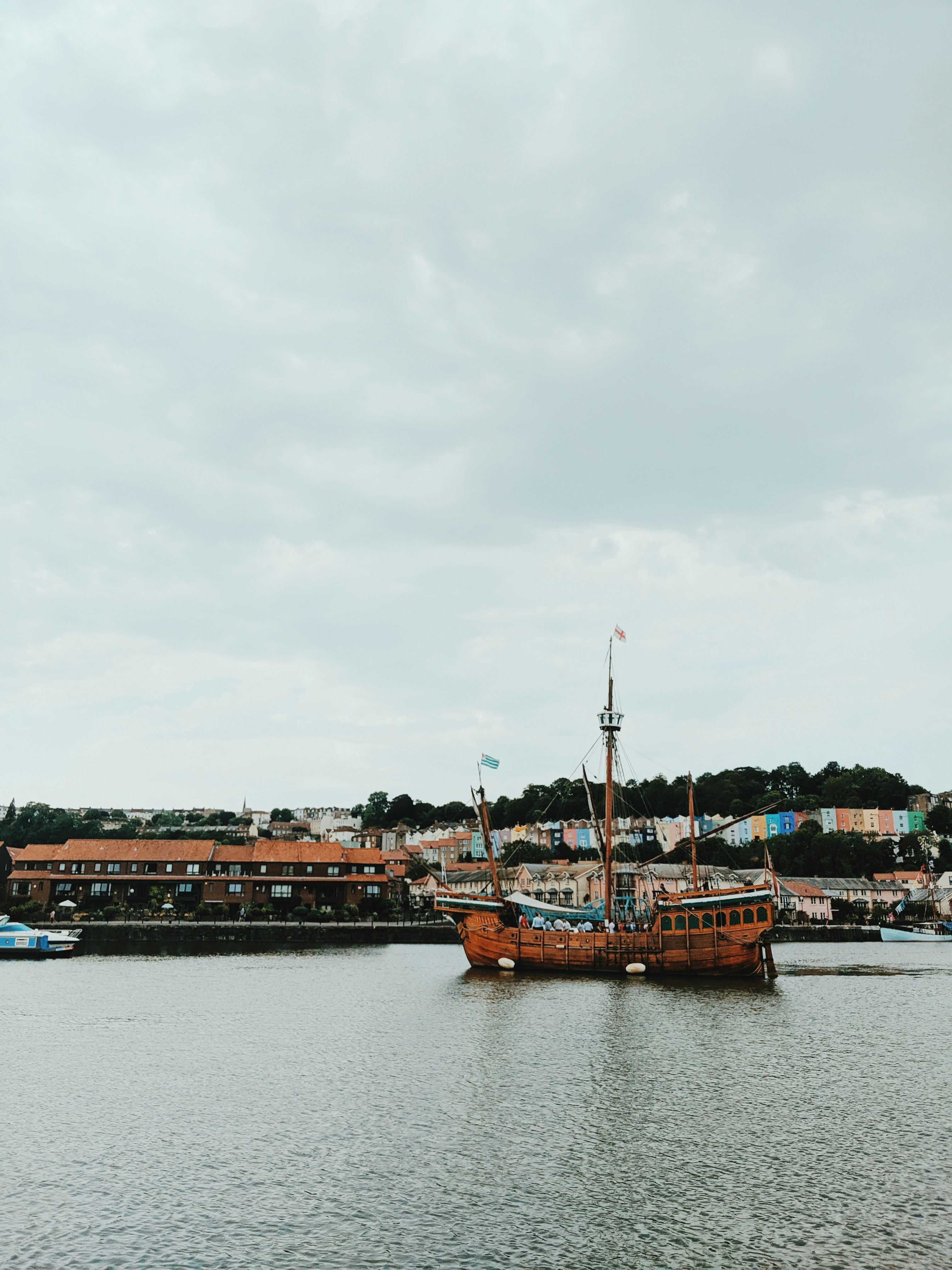 Old ship anchored in a calm harbor under a cloudy sky.