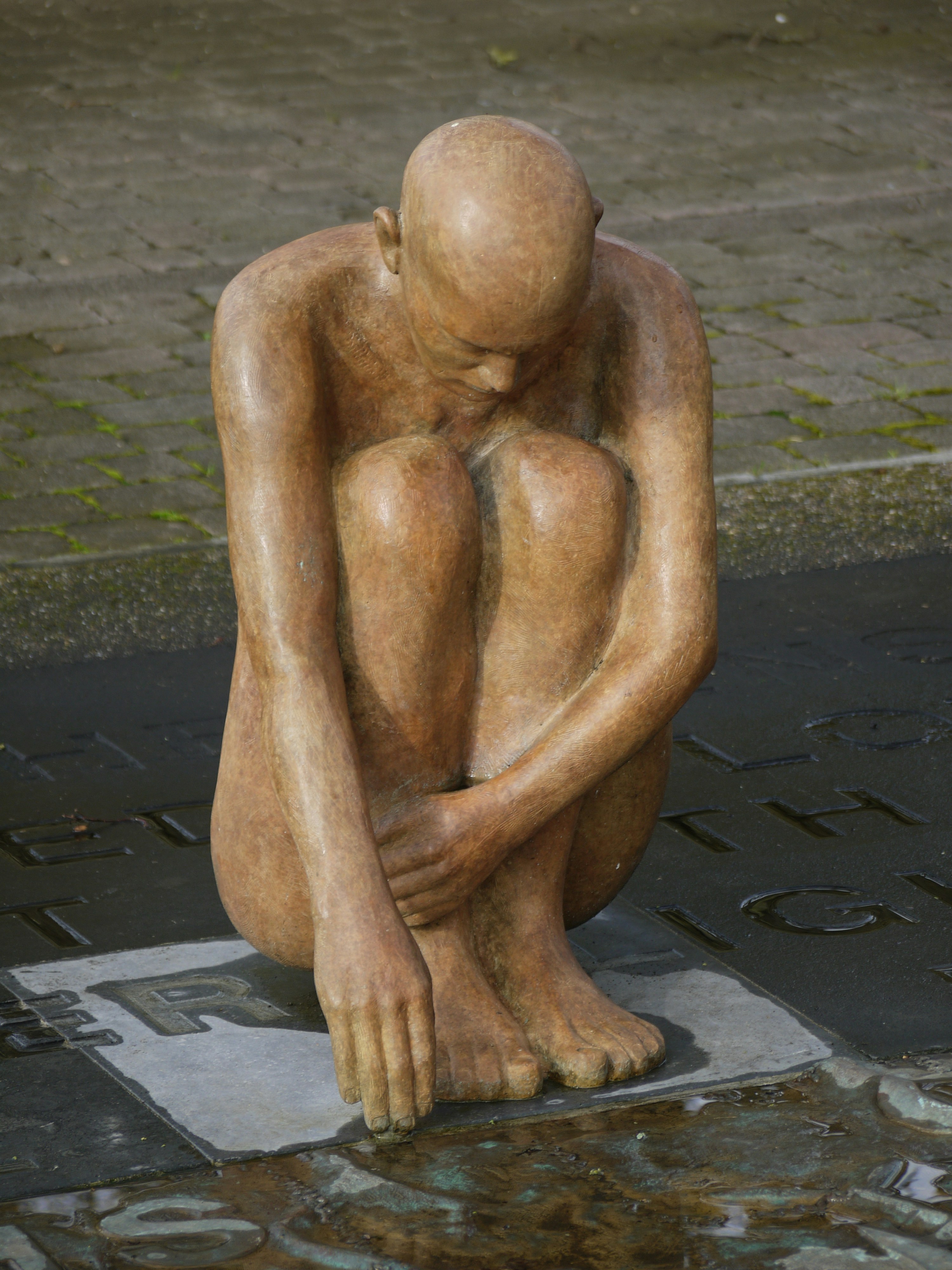A bronze sculpture shows a person in a fetal position.