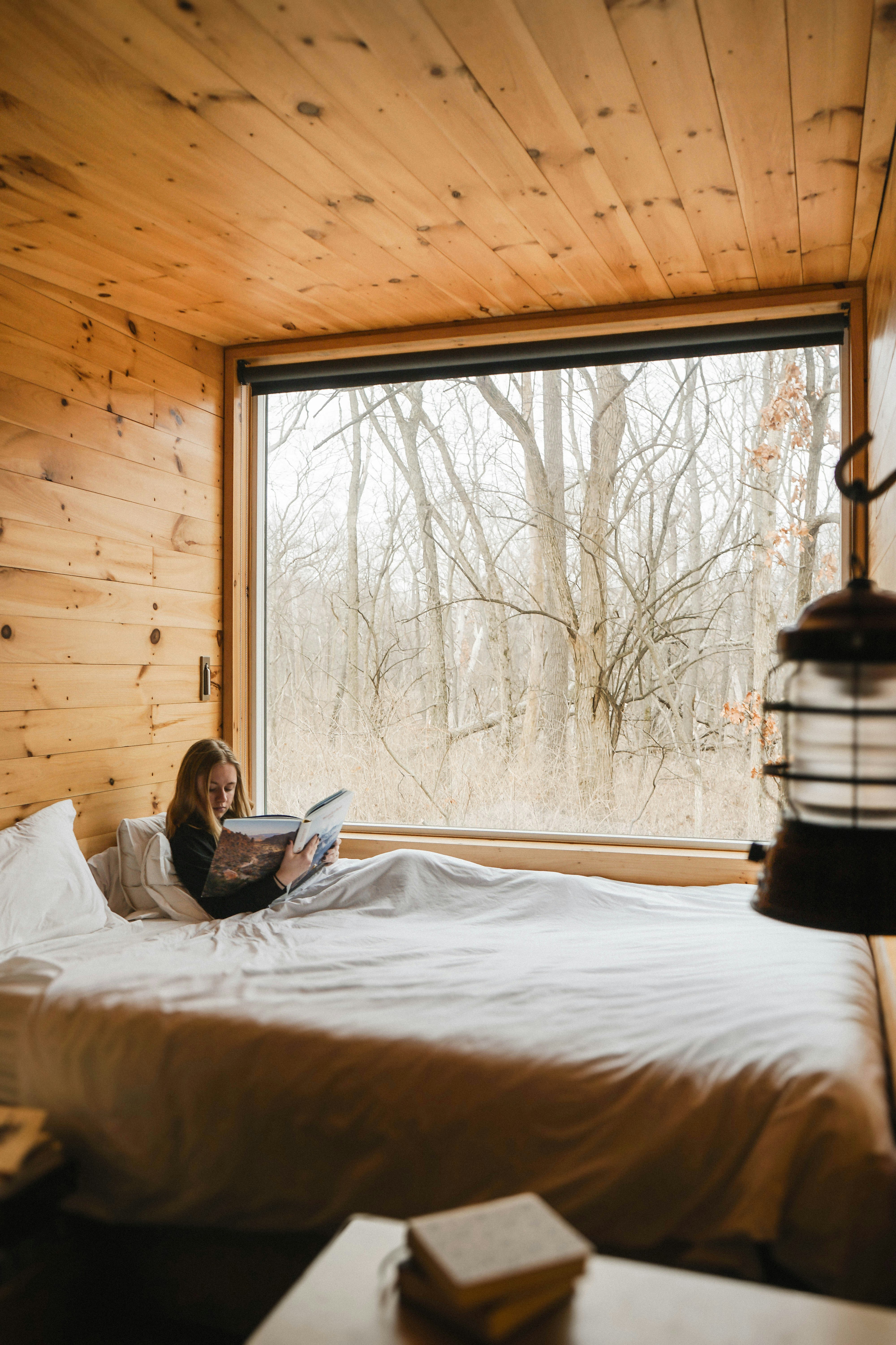 Warm Getaway: A Cozy Reader in a Wood-Filled Bedroom with a Snowy Window View
