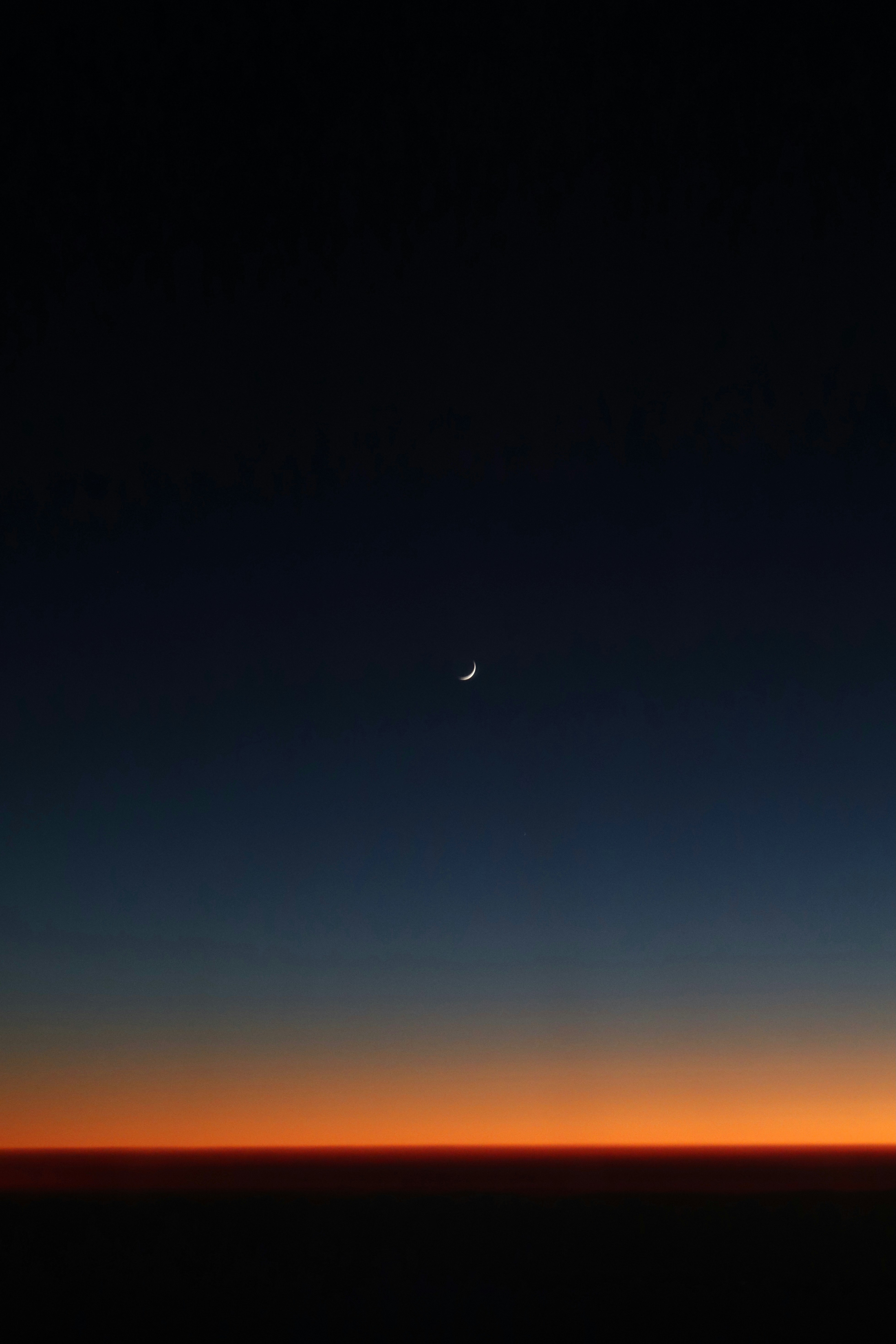 Crescent moon over a gradient twilight horizon, shifting from warm orange near the horizon to deep blue aloft.