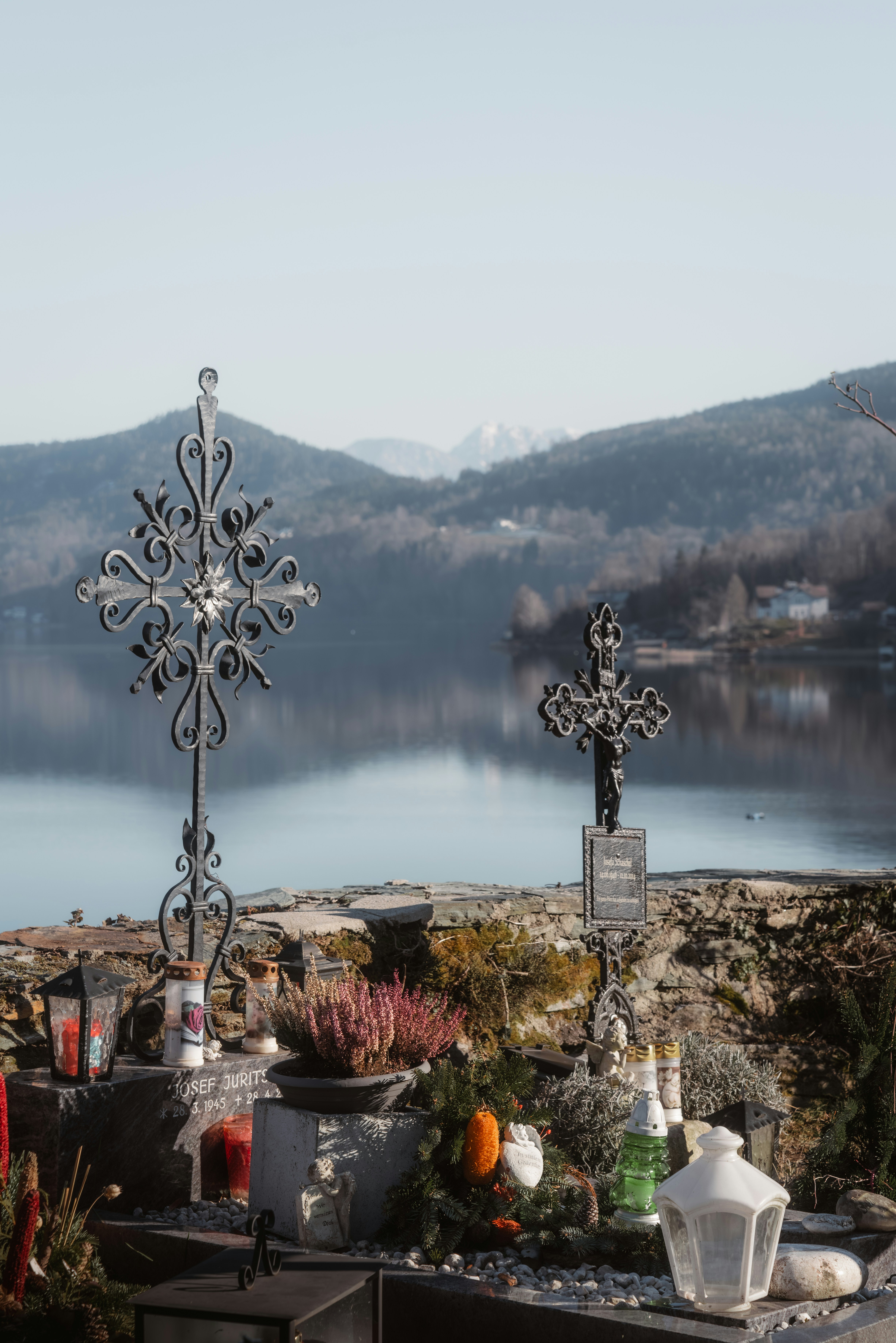 Ornate memorial crosses overlook a tranquil lake with distant mountains under a clear sky.