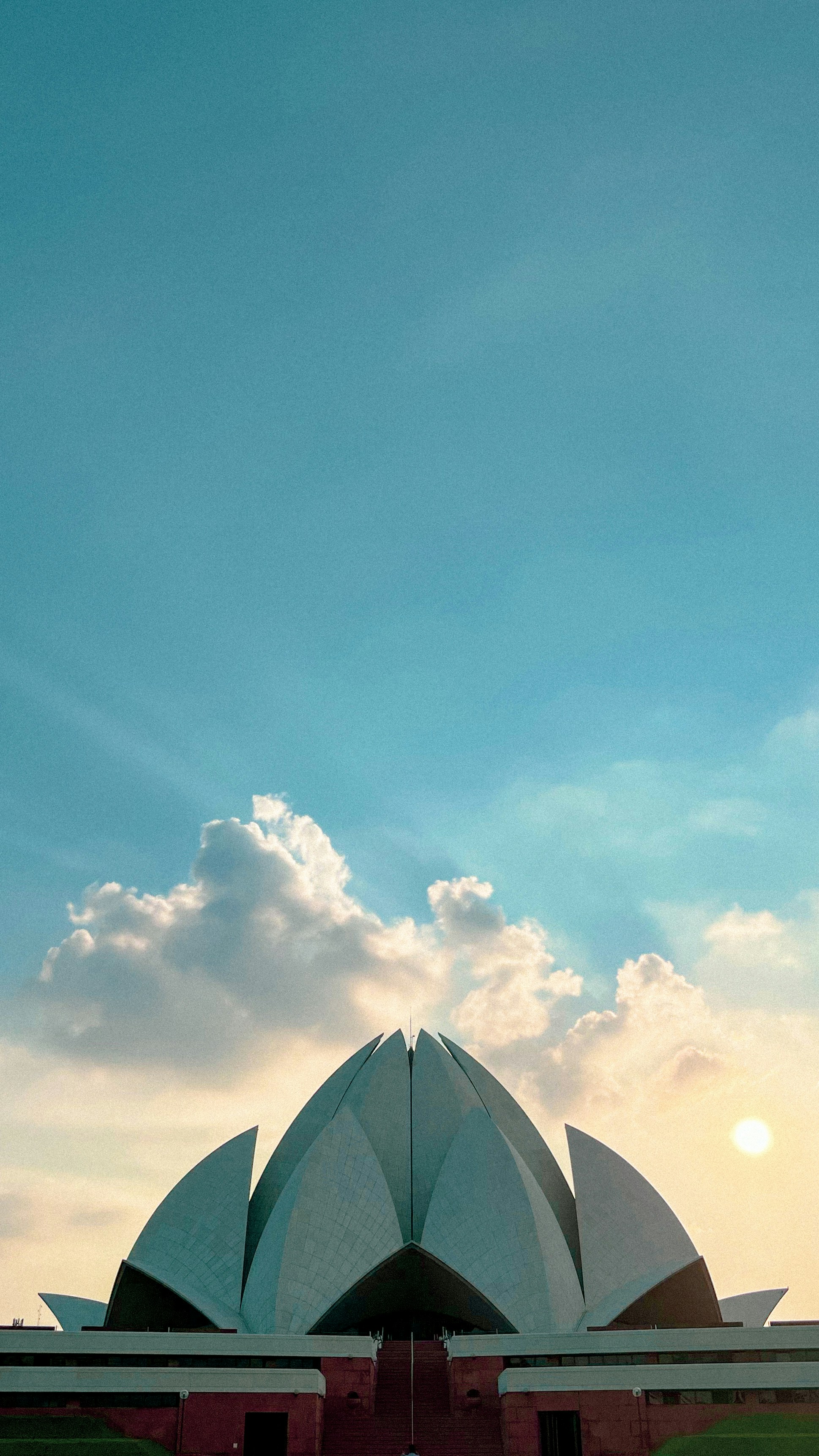The iconic Lotus Temple rises majestically against a backdrop of soft clouds and a setting sun, showcasing its unique architectural design.