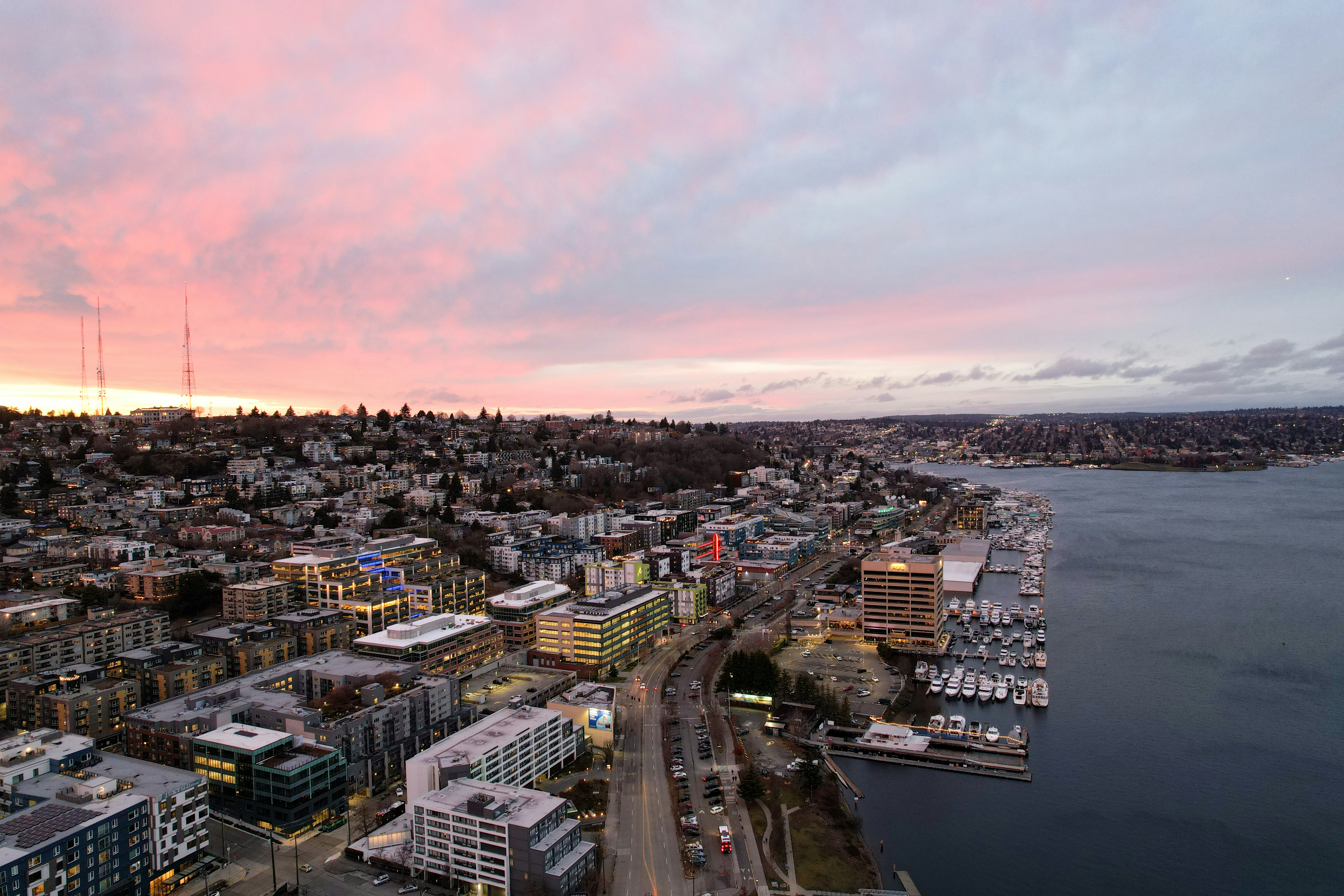 Aerial view of a cityscape with colorful sunset sky reflecting on the waterfront.