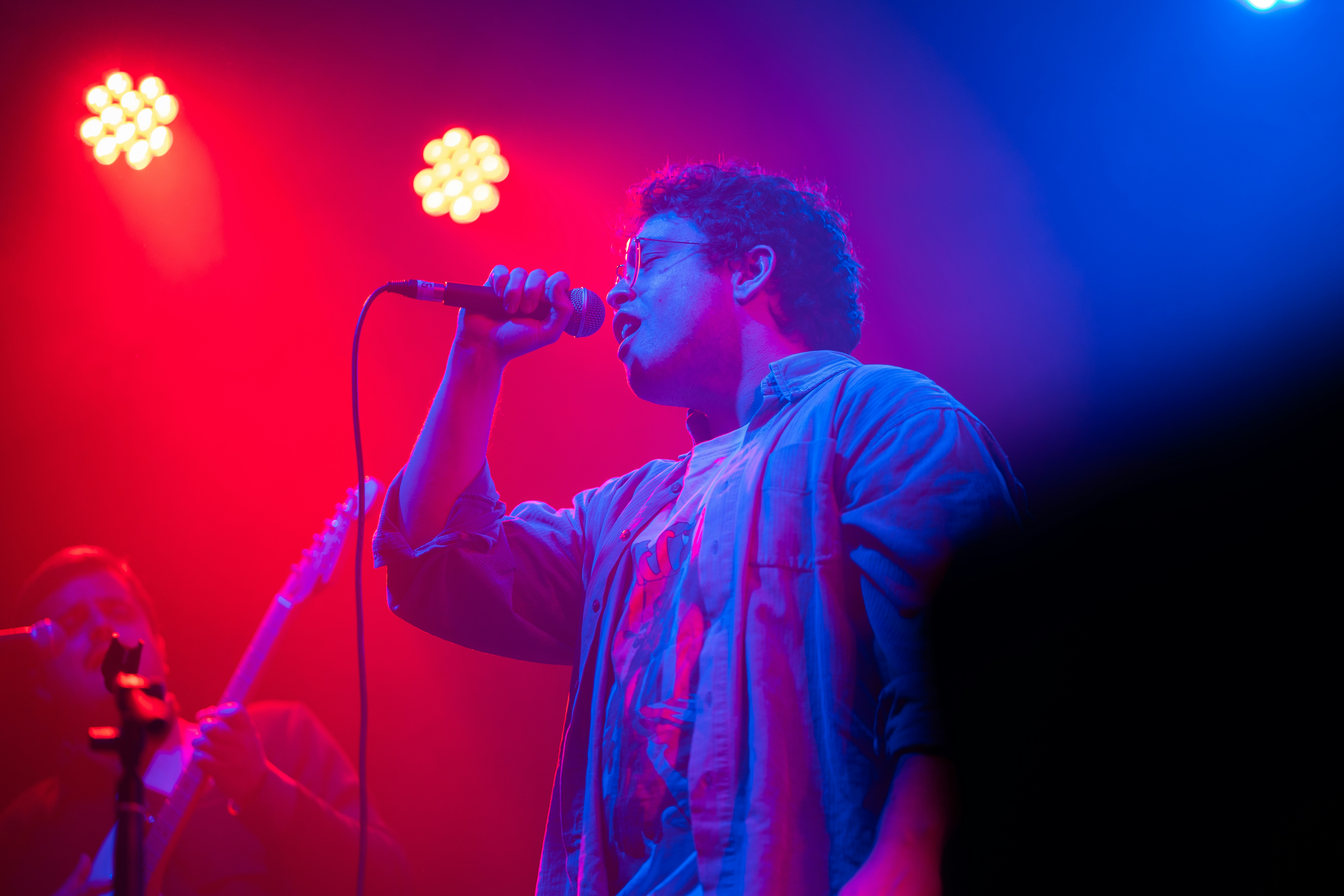 Musician passionately sings under intense red and blue stage lights.