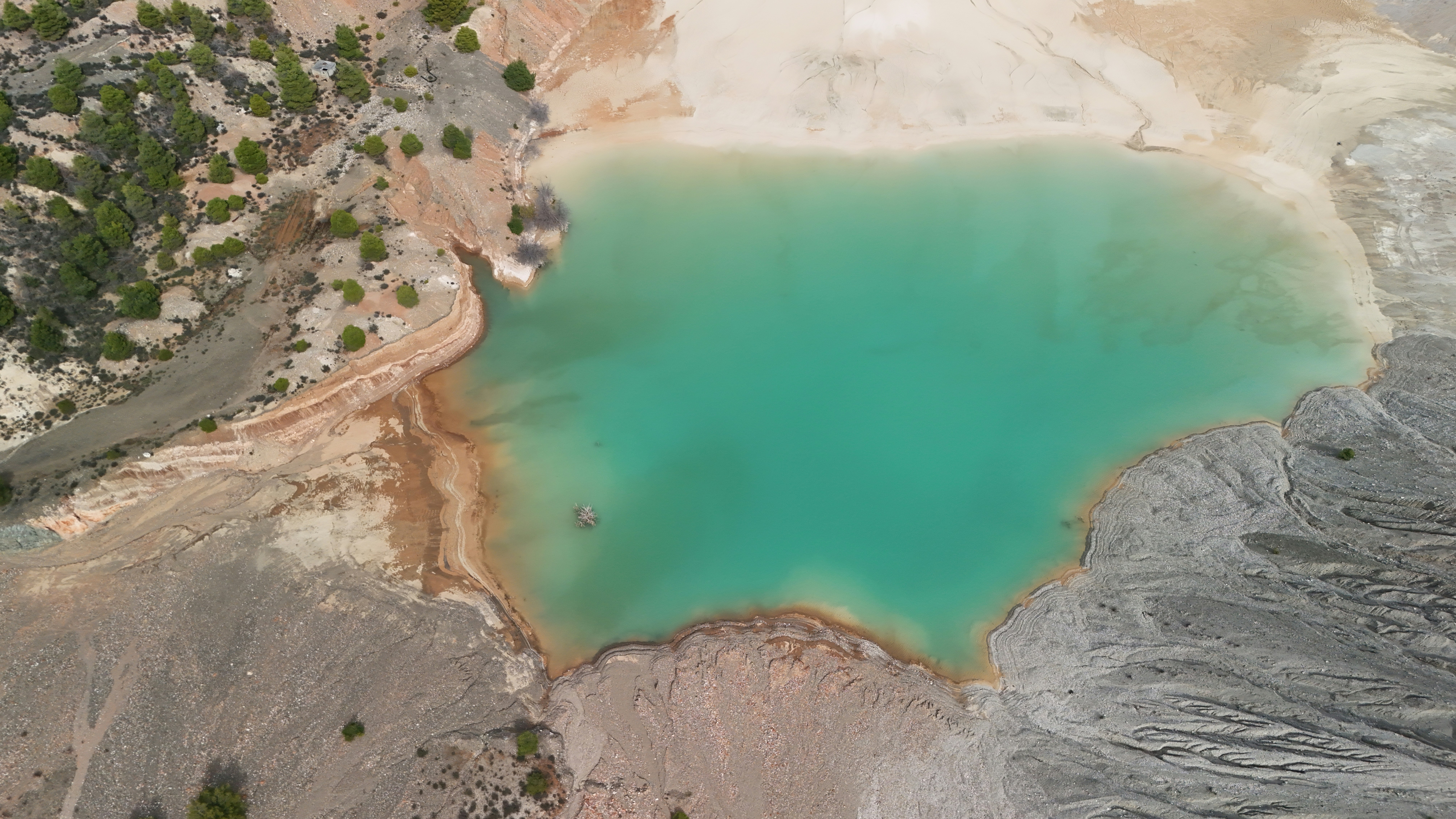 Turquoise lake encircled by rugged, eroded landscape with sparse vegetation.