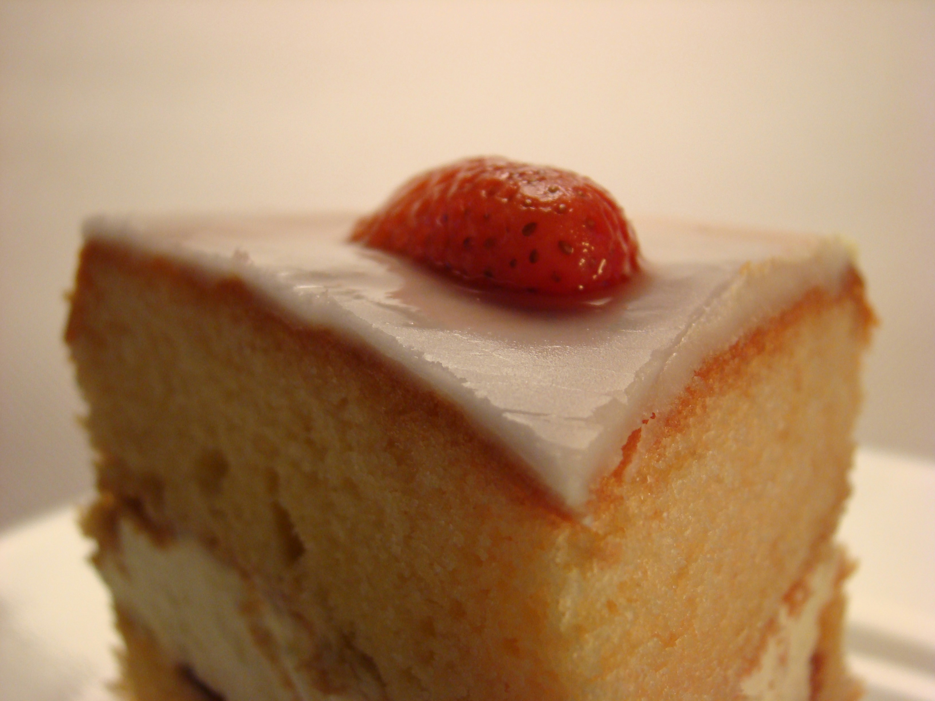 Slice of sponge cake topped with glossy icing and a fresh strawberry garnish.