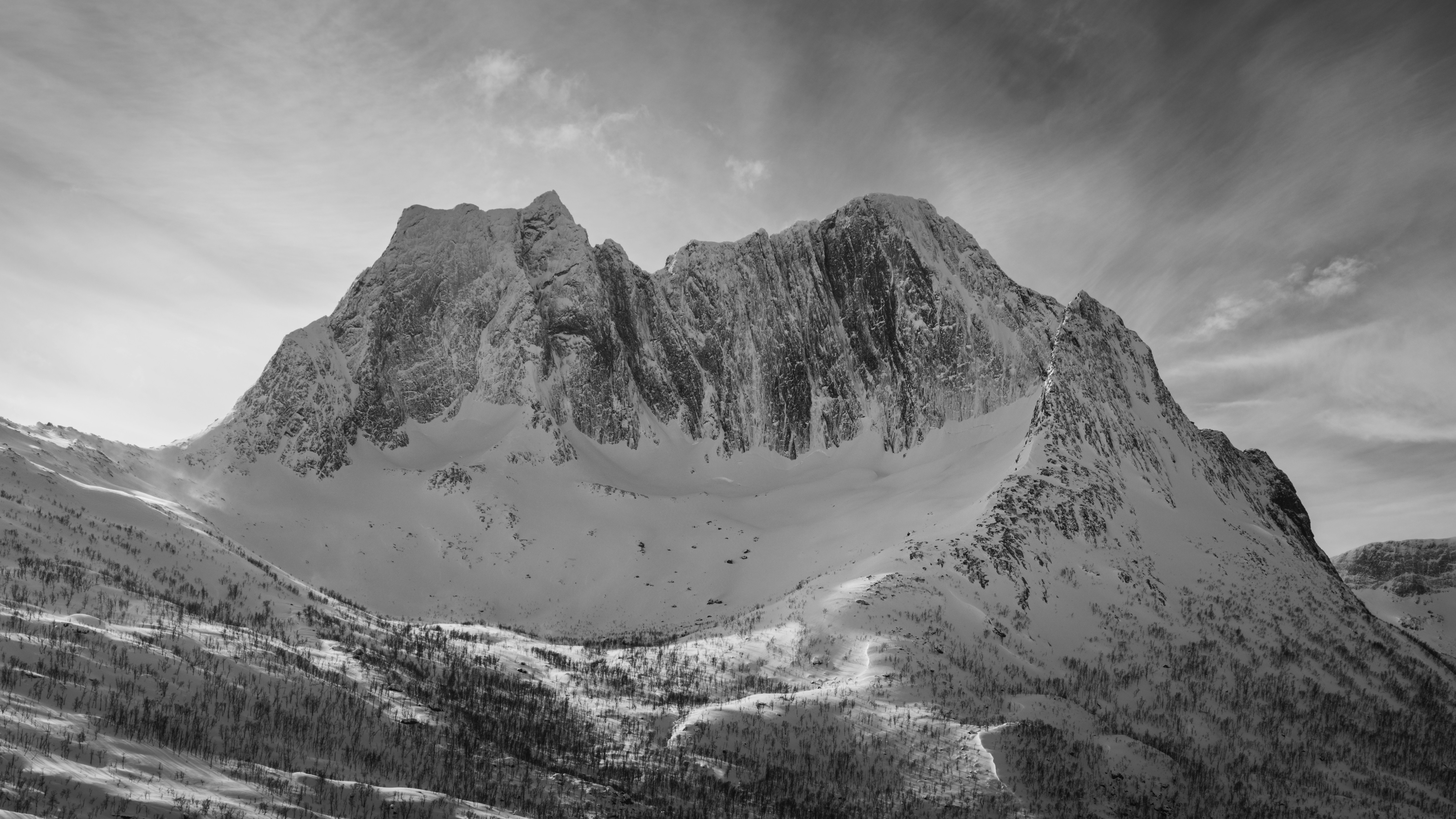 Snow-covered mountains under a cloudy sky with dramatic shadows.