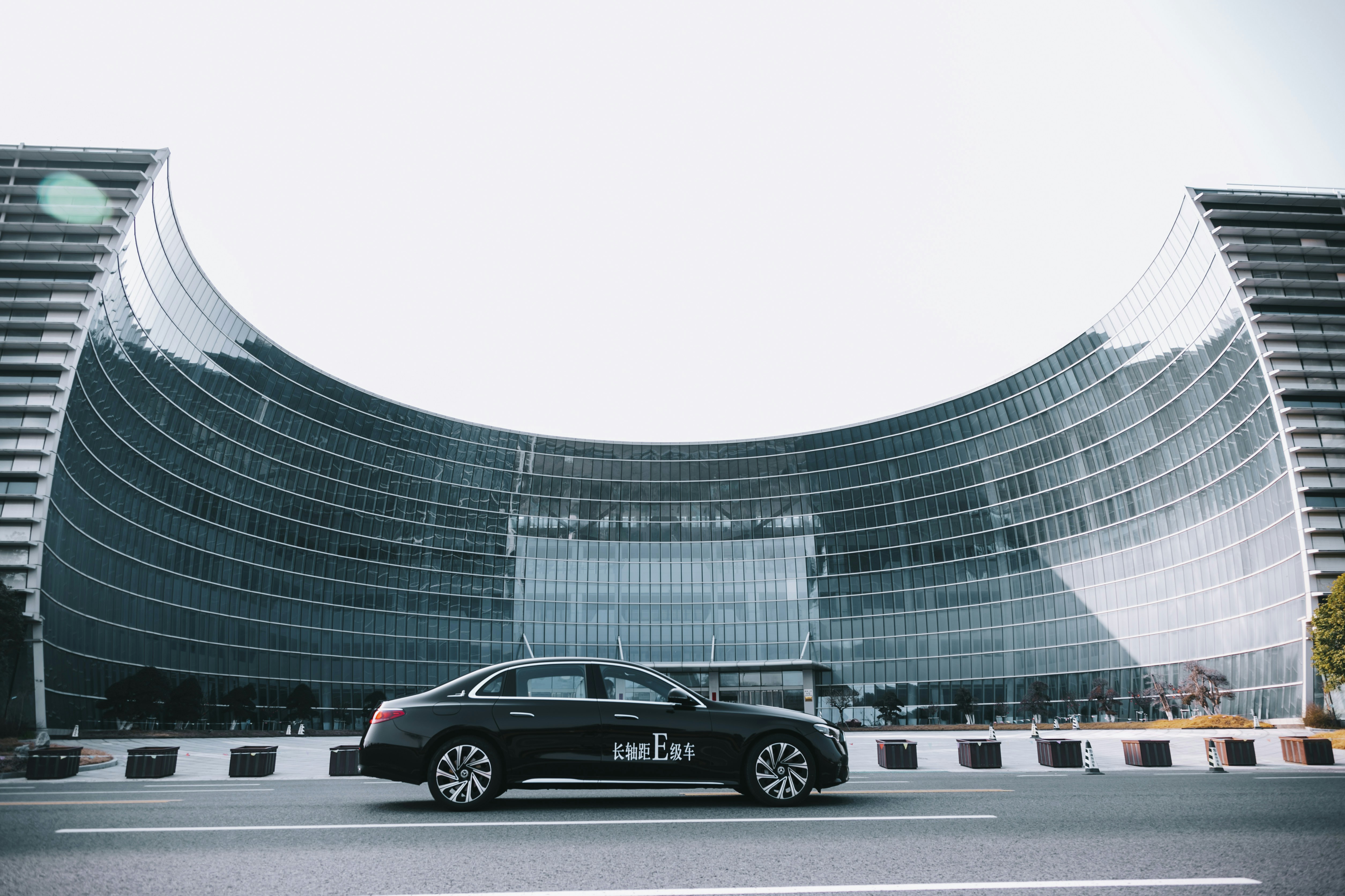 Black sedan parked in front of a modern glass building with curved architecture.
