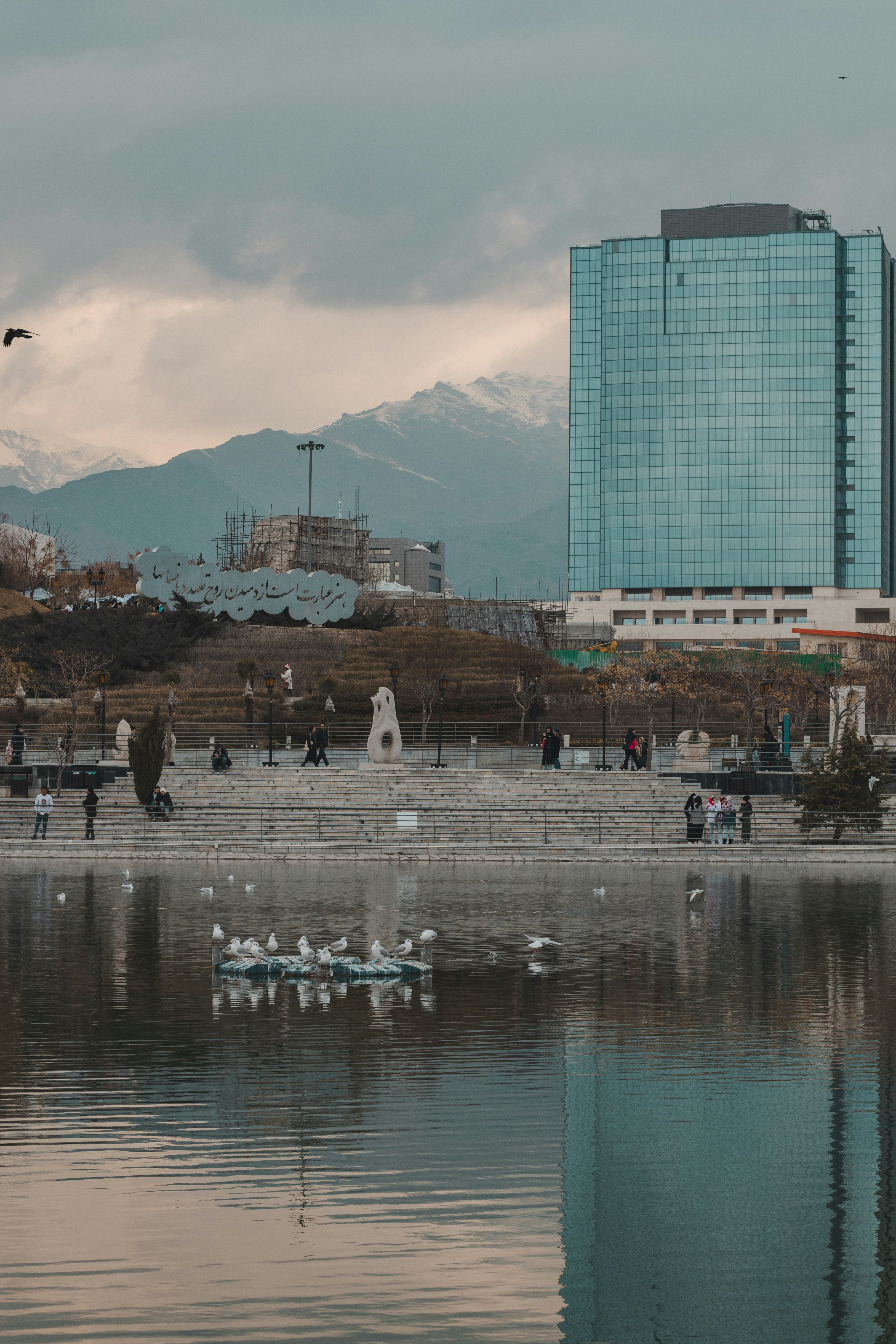 Azure Glass Tower Over a Lakeside Panorama with Snow-Capped Mountains
