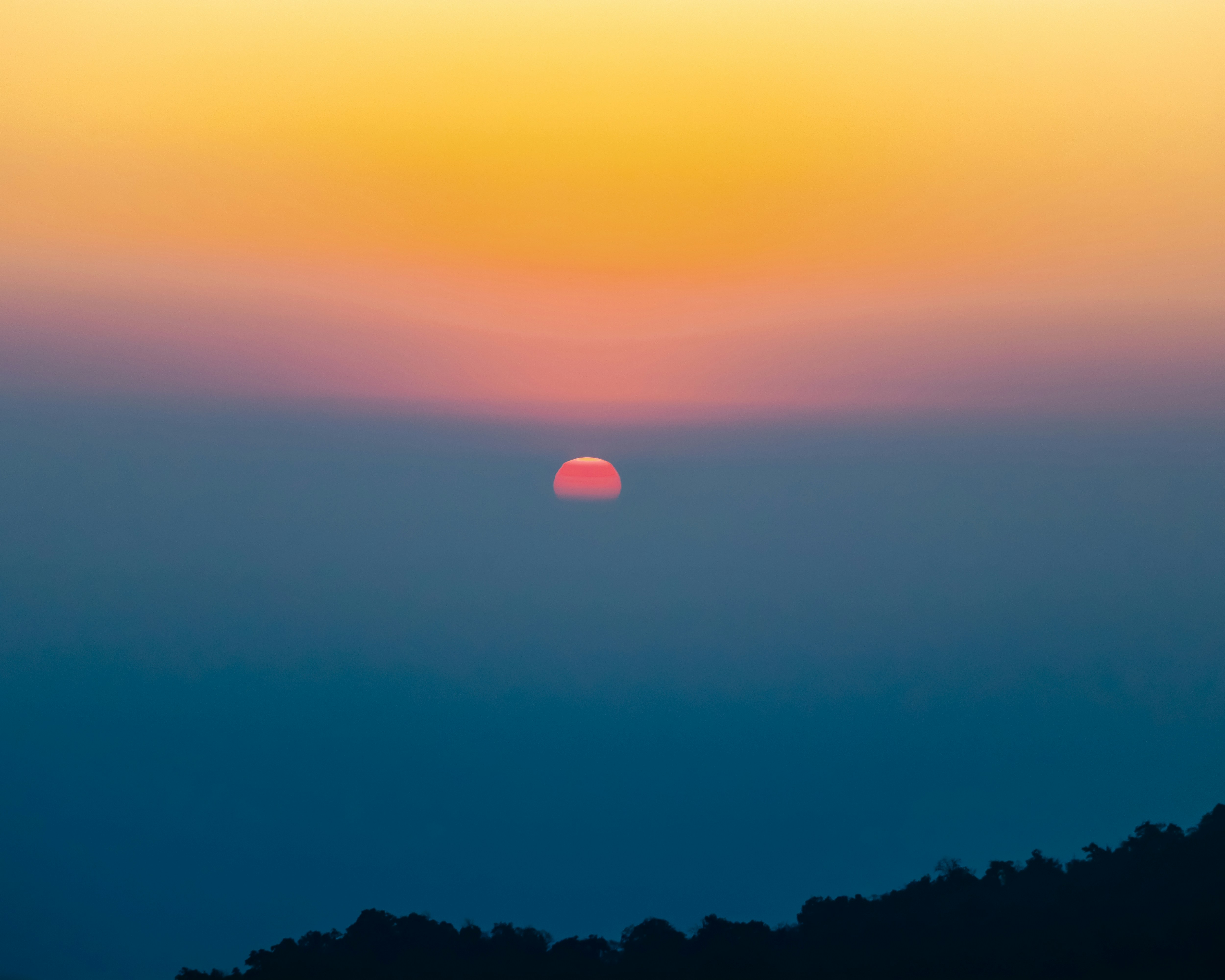 Sun sets against a gradient sky transitioning from orange to deep blue above silhouetted hills.