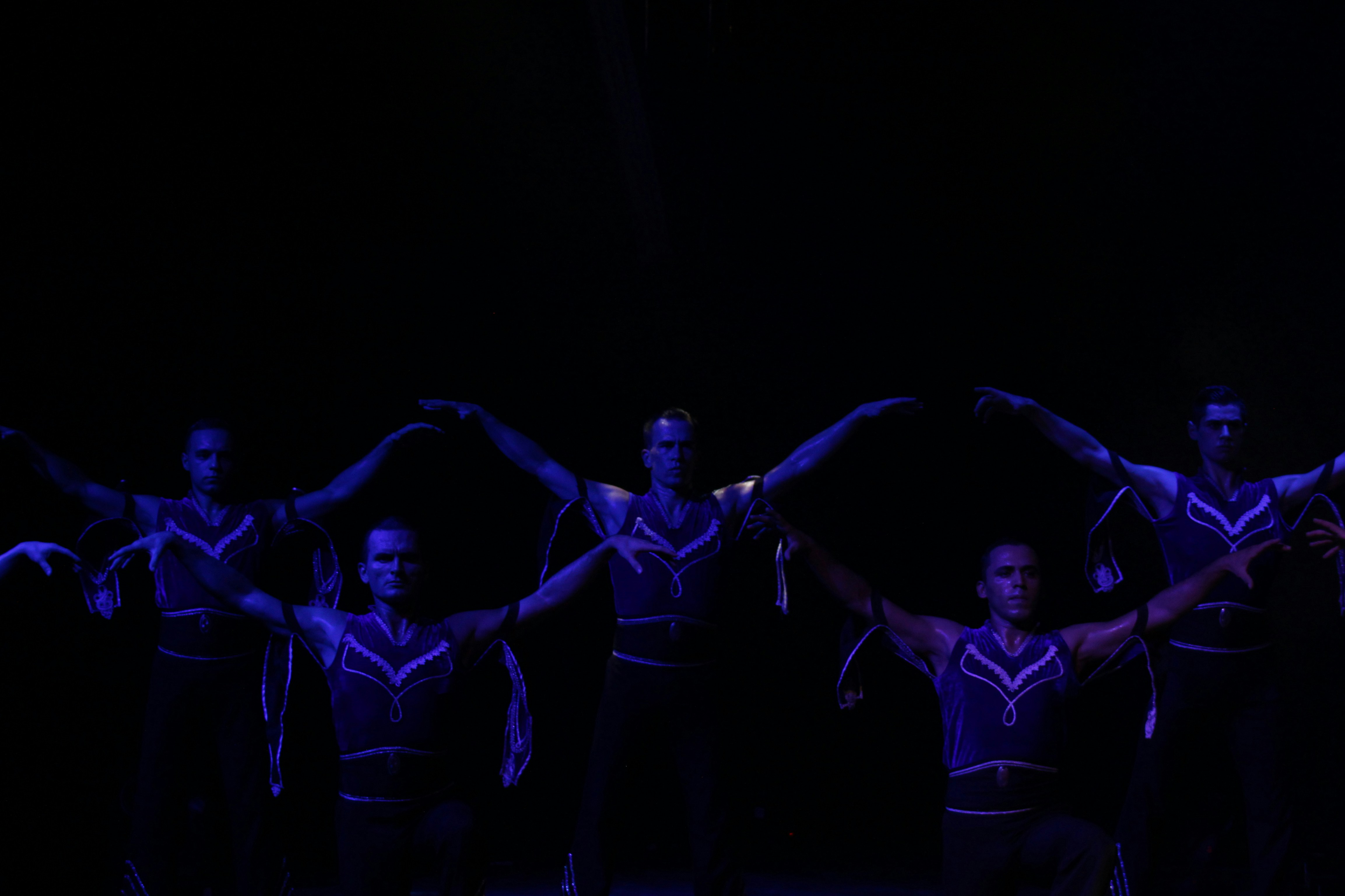 Group of male dancers striking dynamic poses under dramatic blue lighting, showcasing their athleticism and artistry.