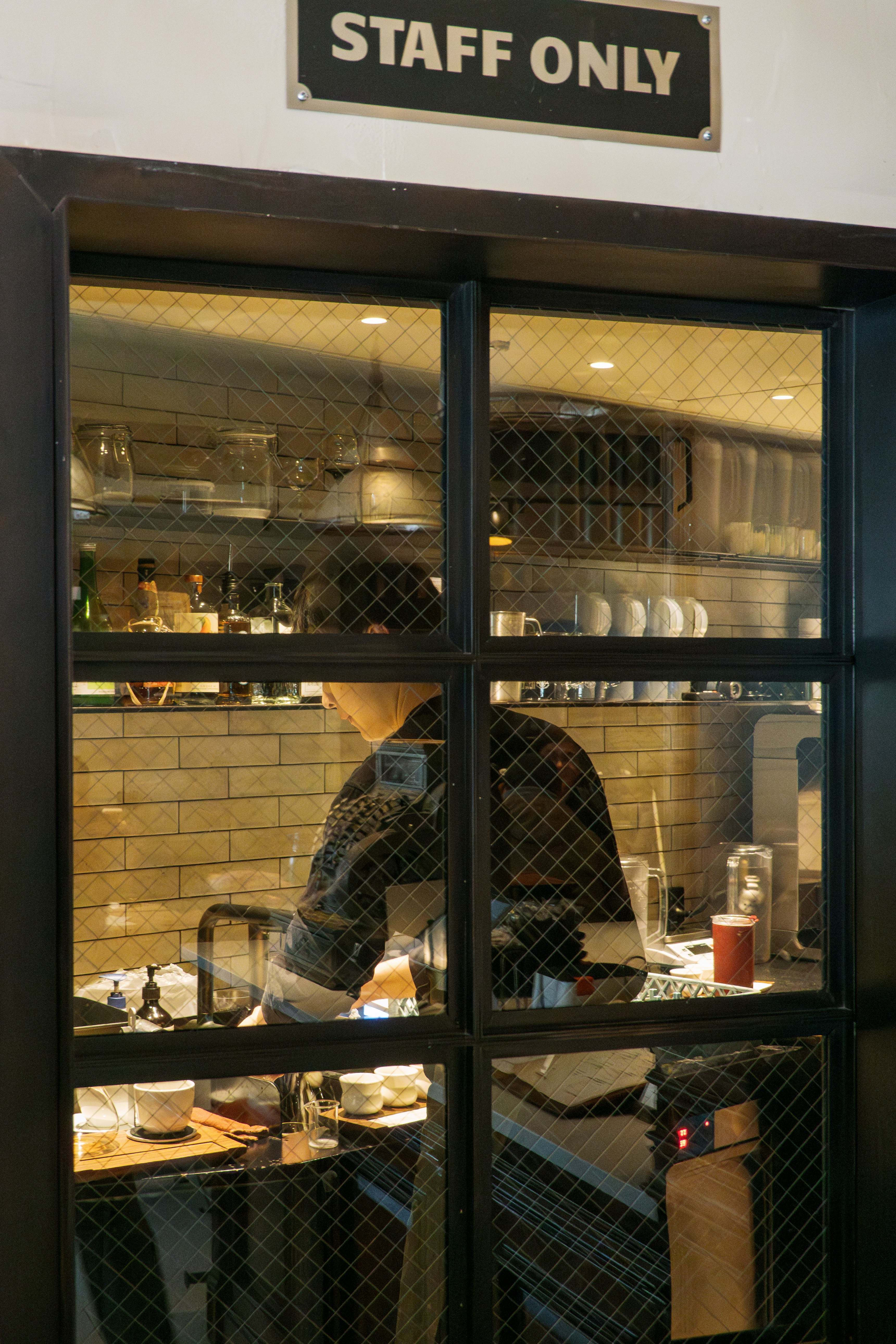 Gridded Focus: A Chef at Work Through a Wire Mesh Window