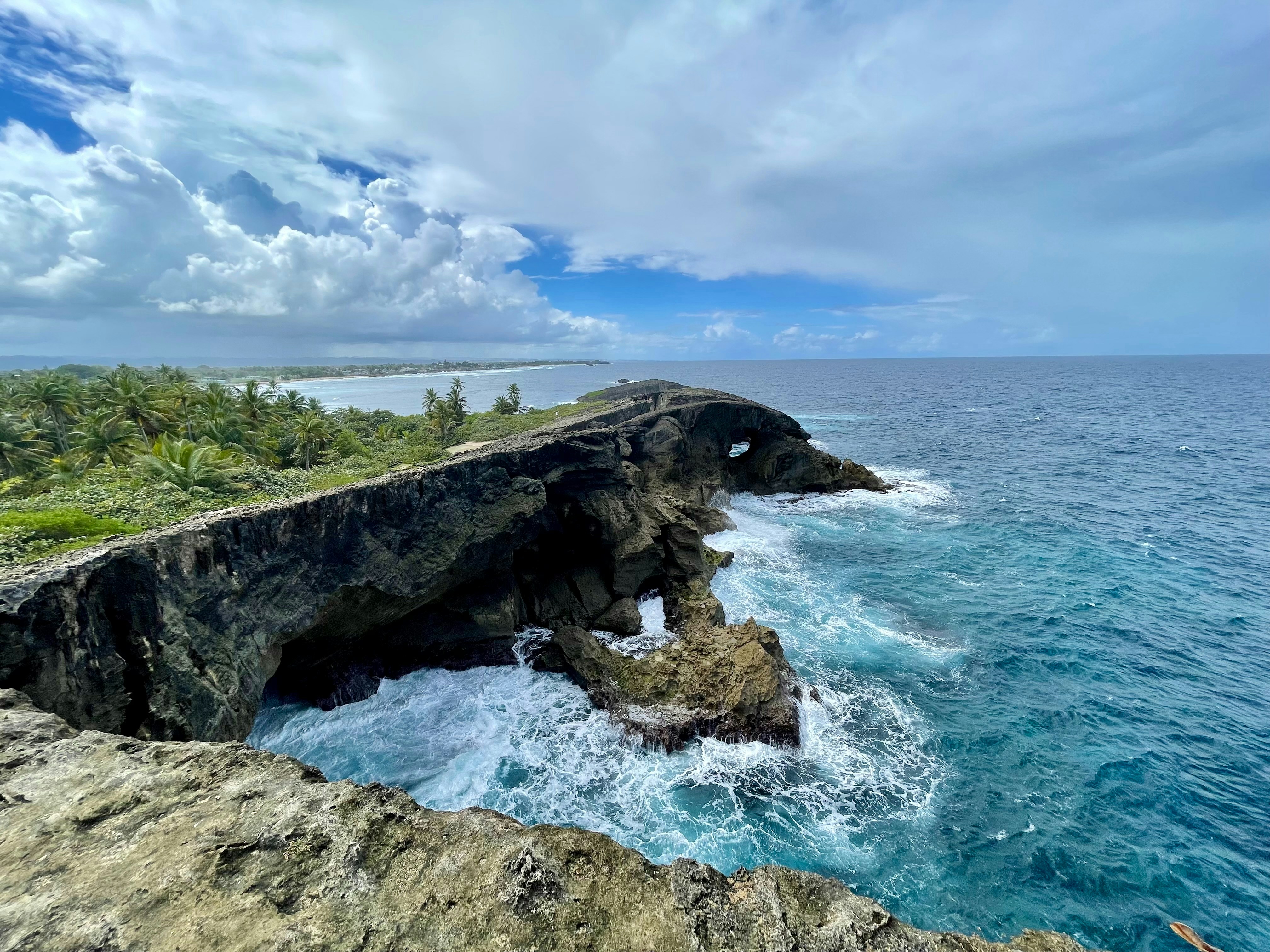 Dramatic coastal rock formations meet the vibrant blue of the Atlantic Ocean under a partly cloudy sky.