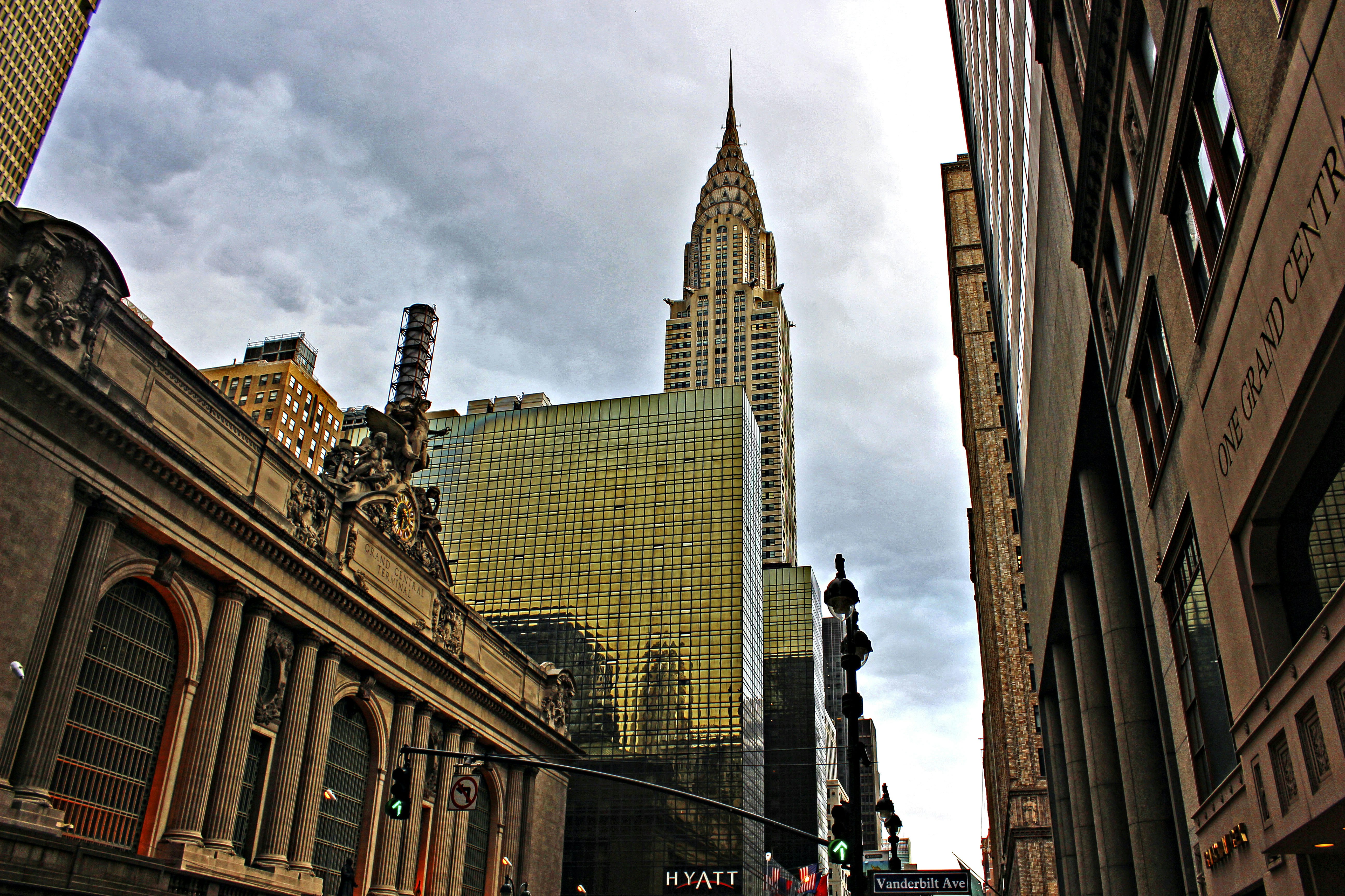 Chrysler Building and surrounding skyscrapers under a cloudy sky viewed from street level.