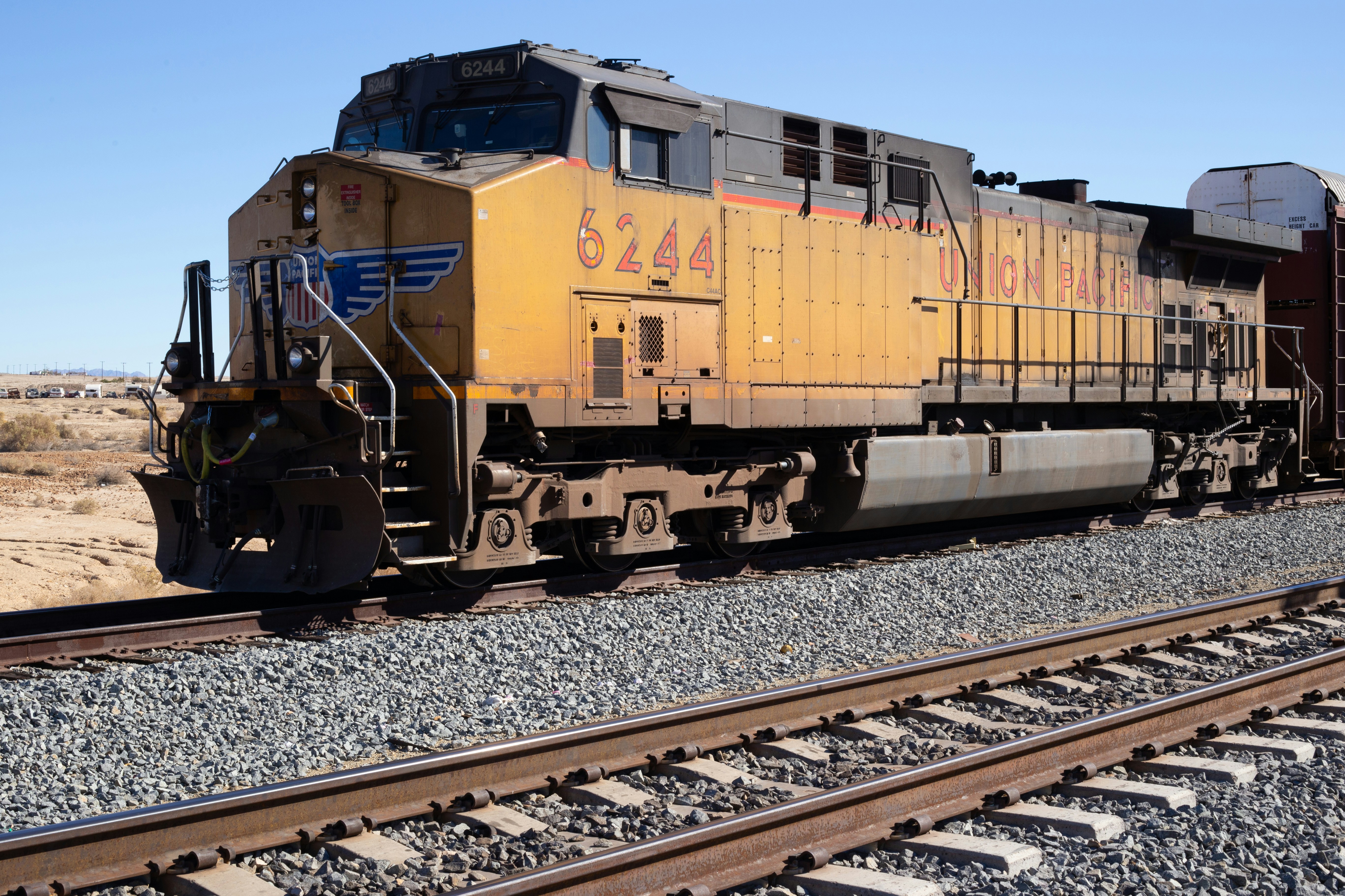 Freight train locomotive traversing a sunlit desert landscape on a clear day.