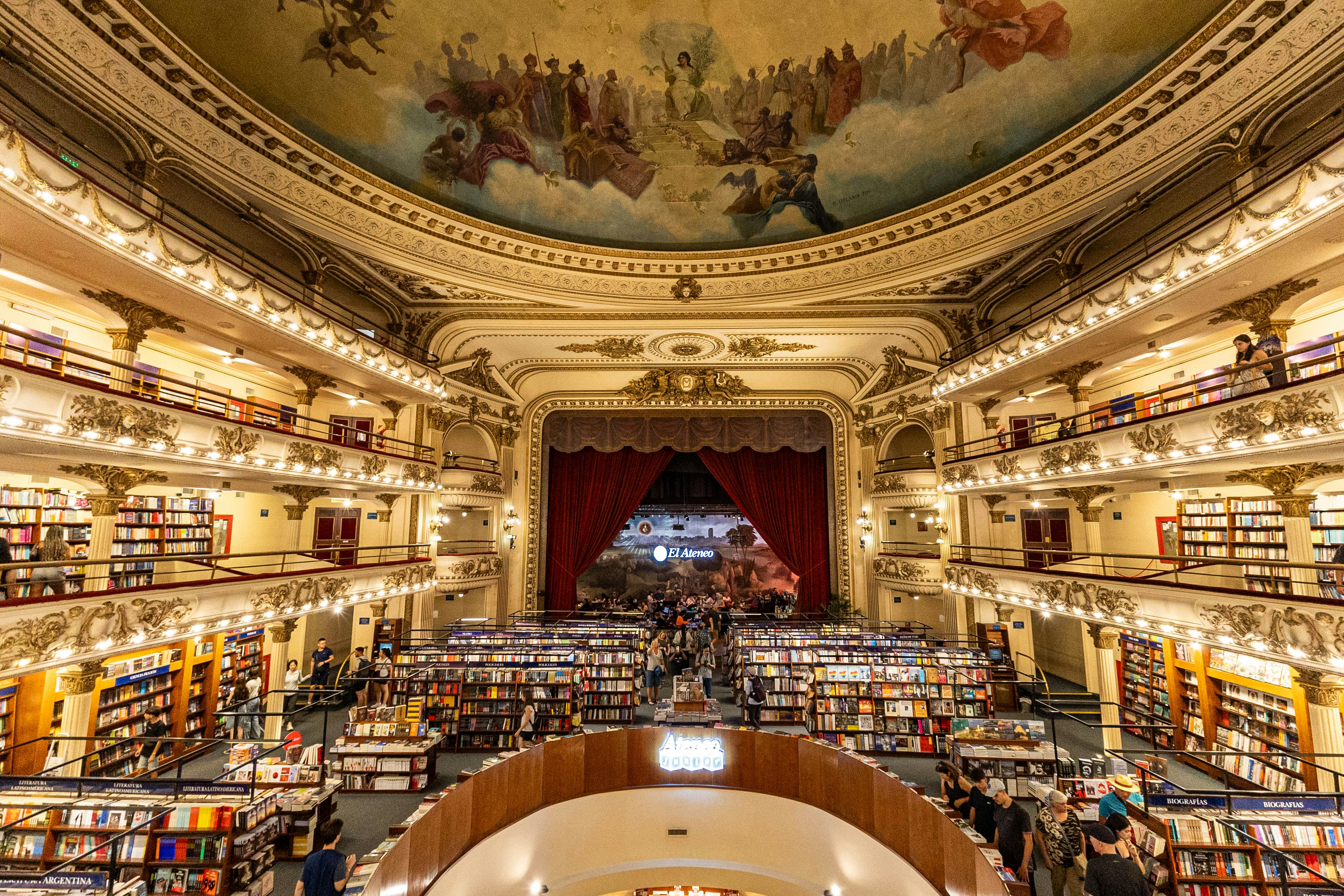 Lavish bookstore housed within an ornate theater, showcasing tiers of books beneath a grand painted ceiling.