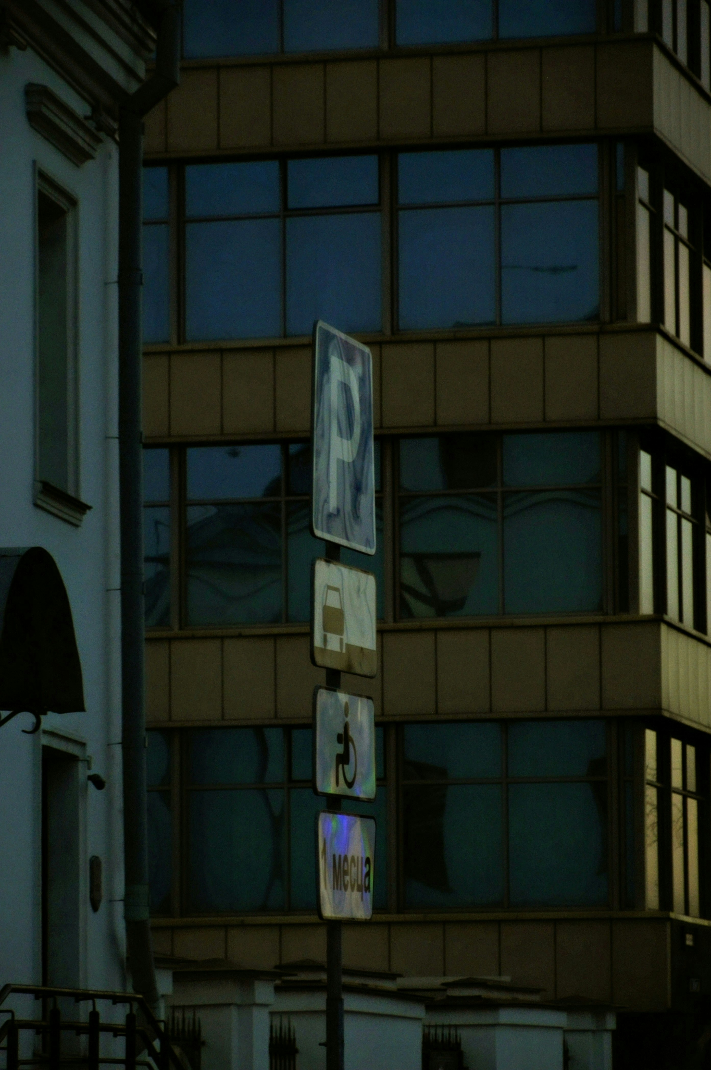 Vertical Sign Stack at Dusk Before a Glass-Fronted Office Block