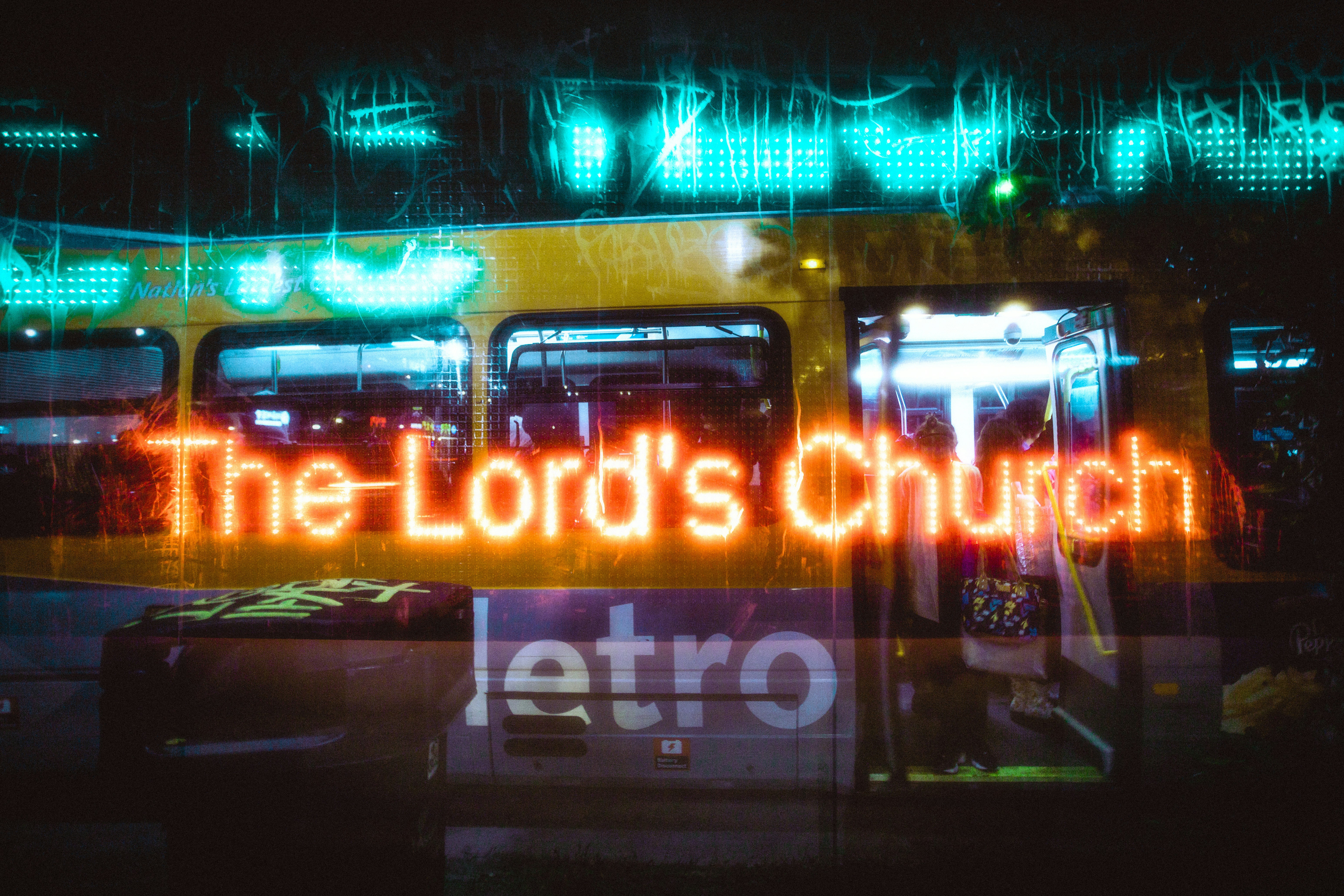 Neon text reflects vividly on a city bus in an urban nightscape.