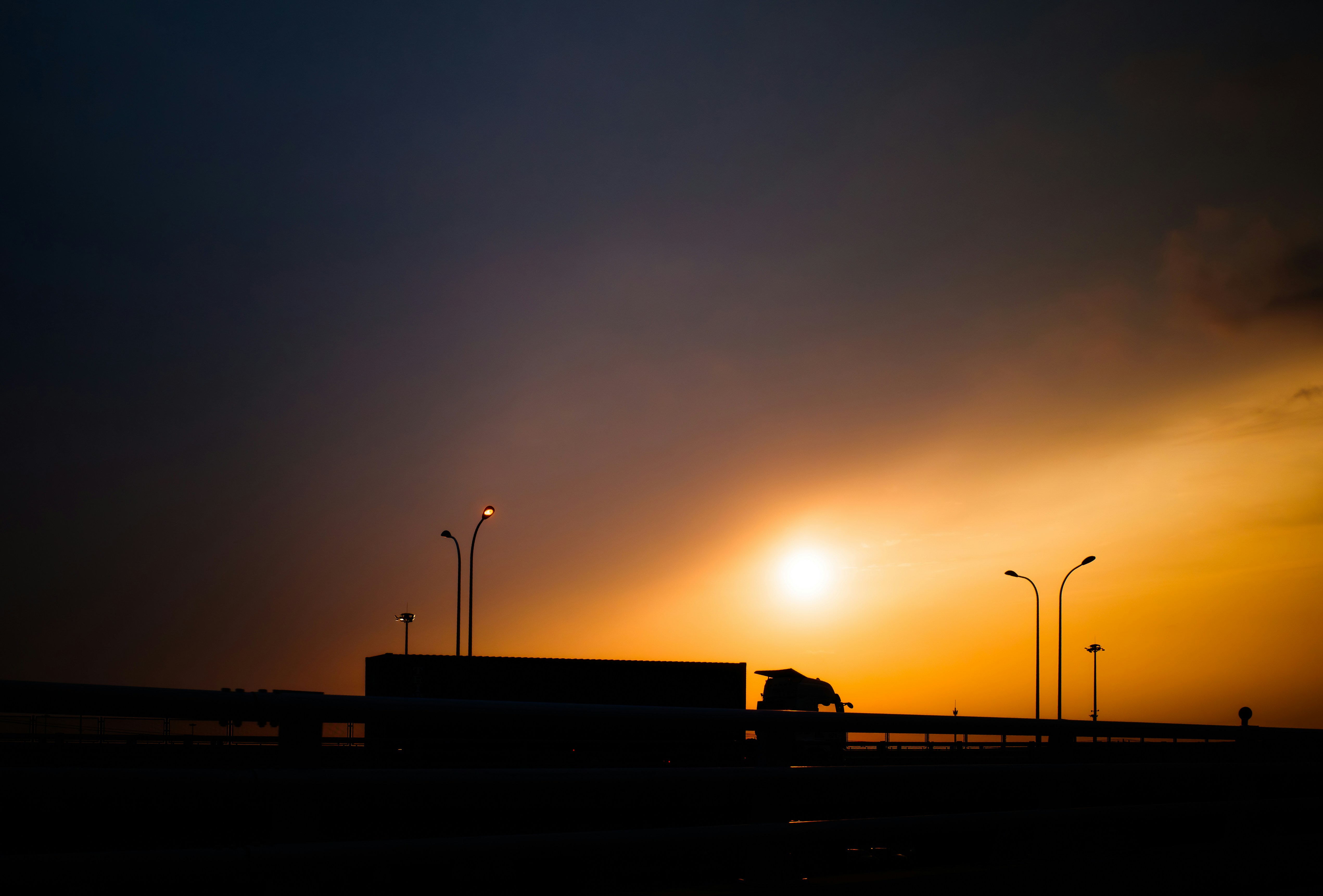 Truck silhouette against a vibrant sunset sky on a highway.