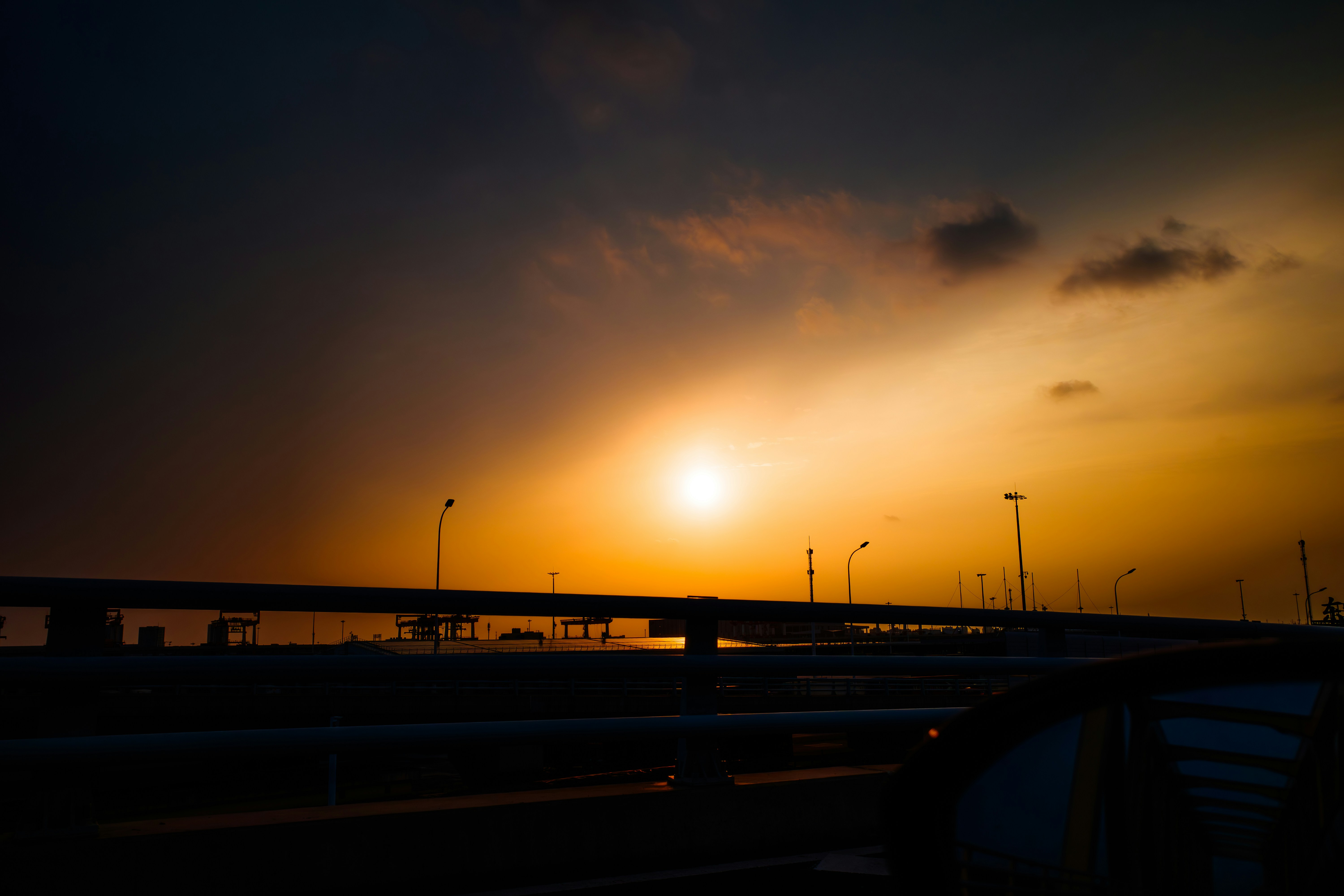 Sunset casting warm hues over a highway bridge with silhouetted streetlights and structures.