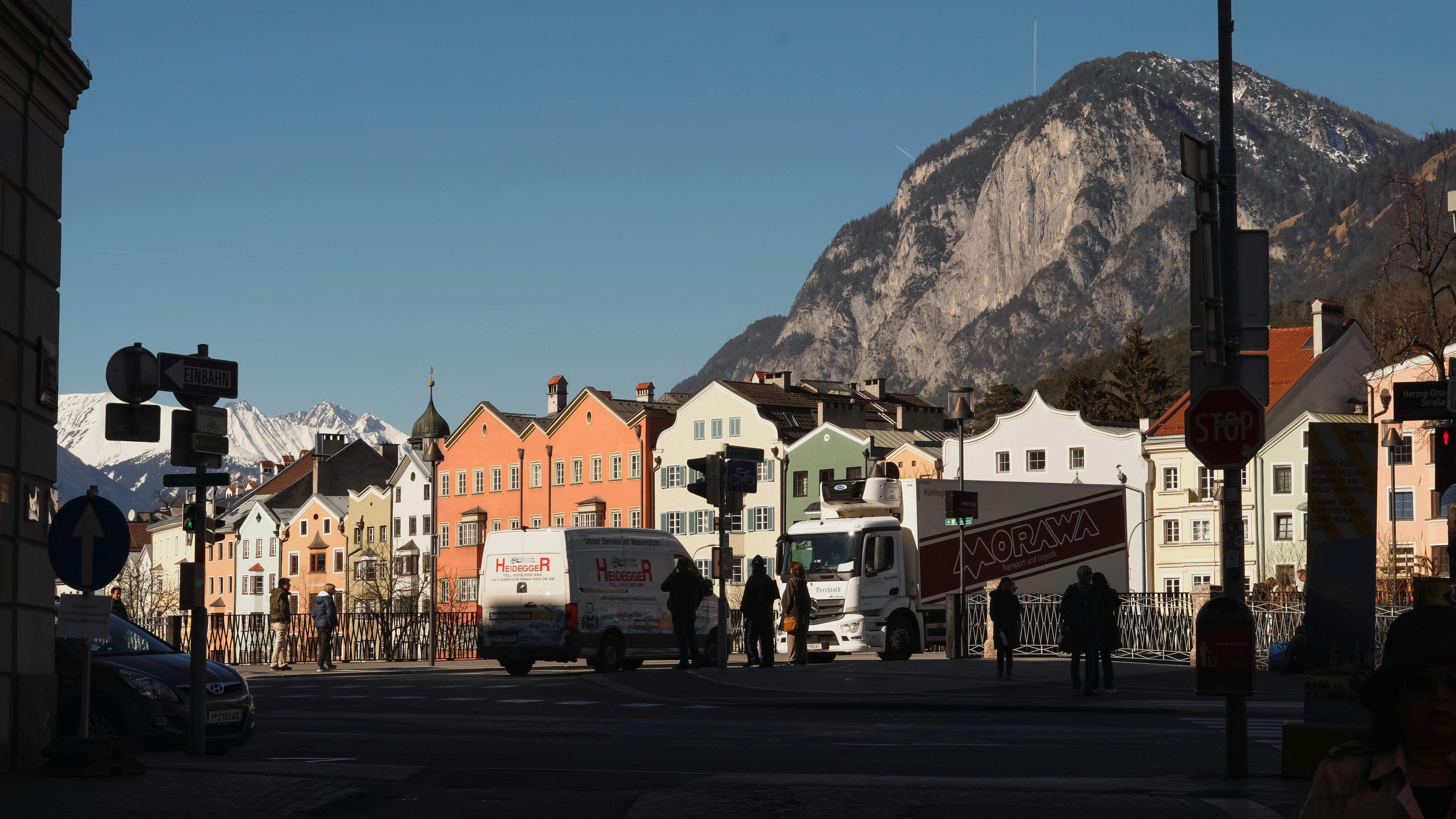 Colorful buildings line a street against a backdrop of towering mountains under a clear blue sky.