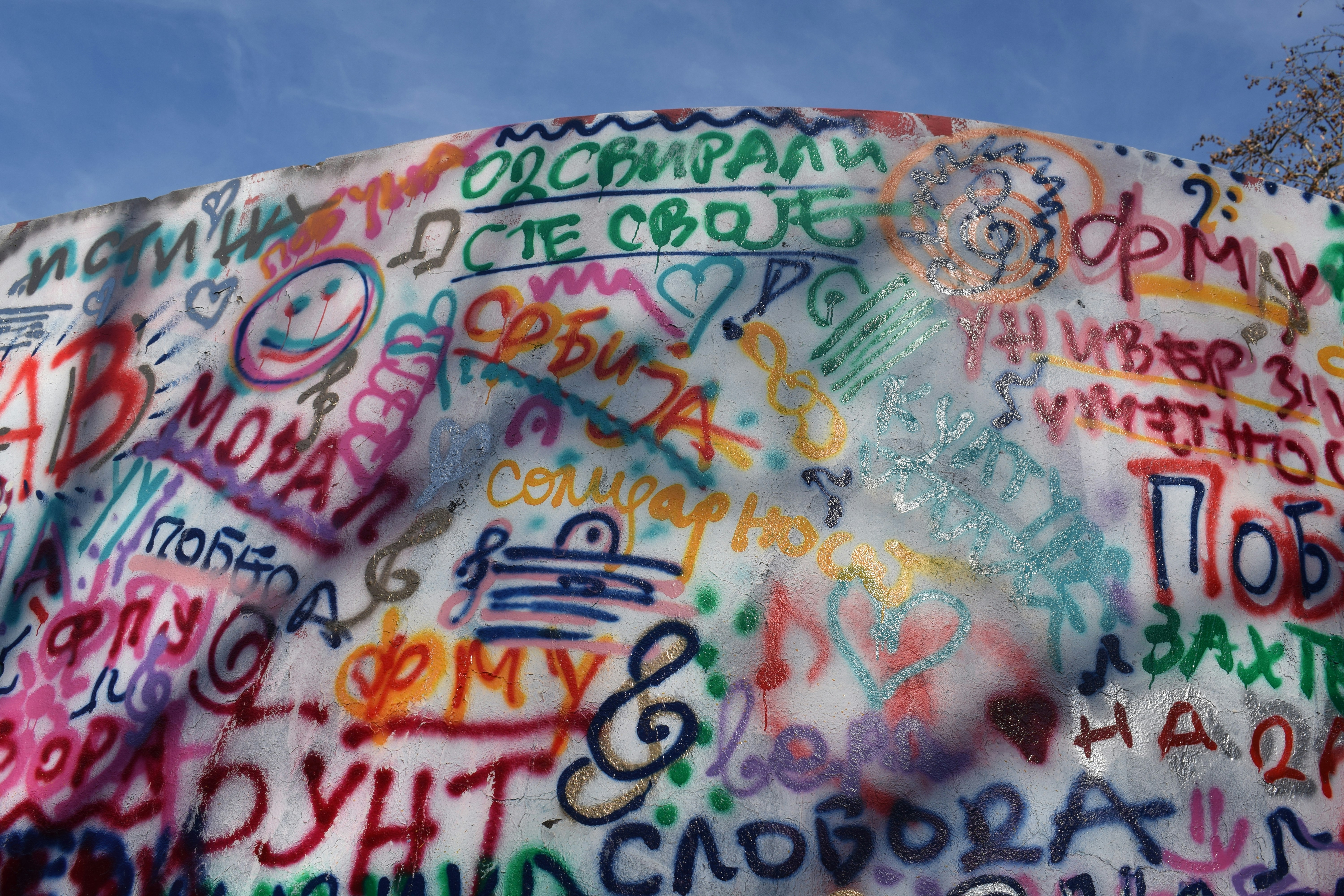 Curved Canvas: Multilingual Graffiti Mosaic Under a Bright Sky