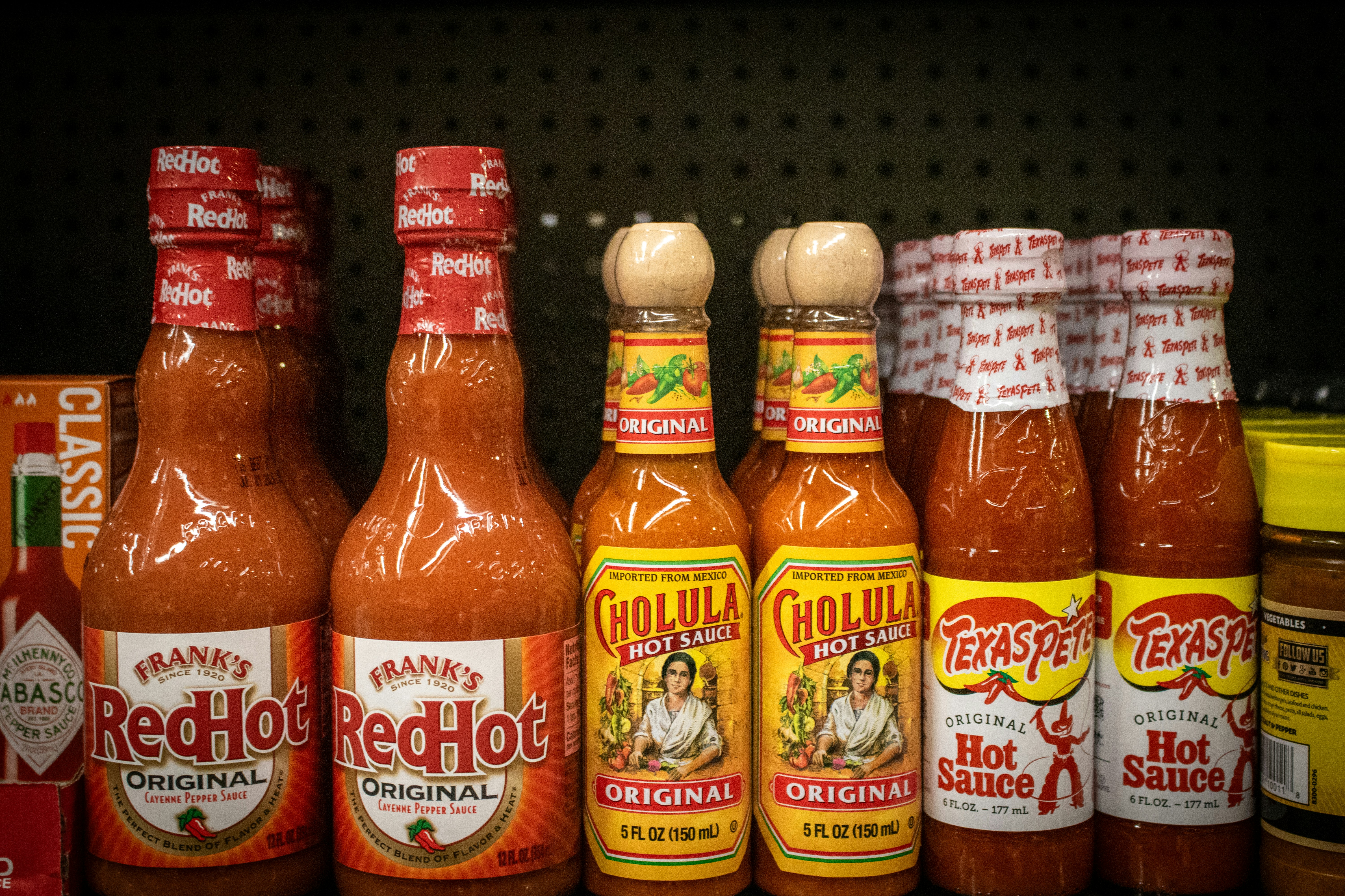 Variety of hot sauce bottles neatly lined up on a grocery shelf.