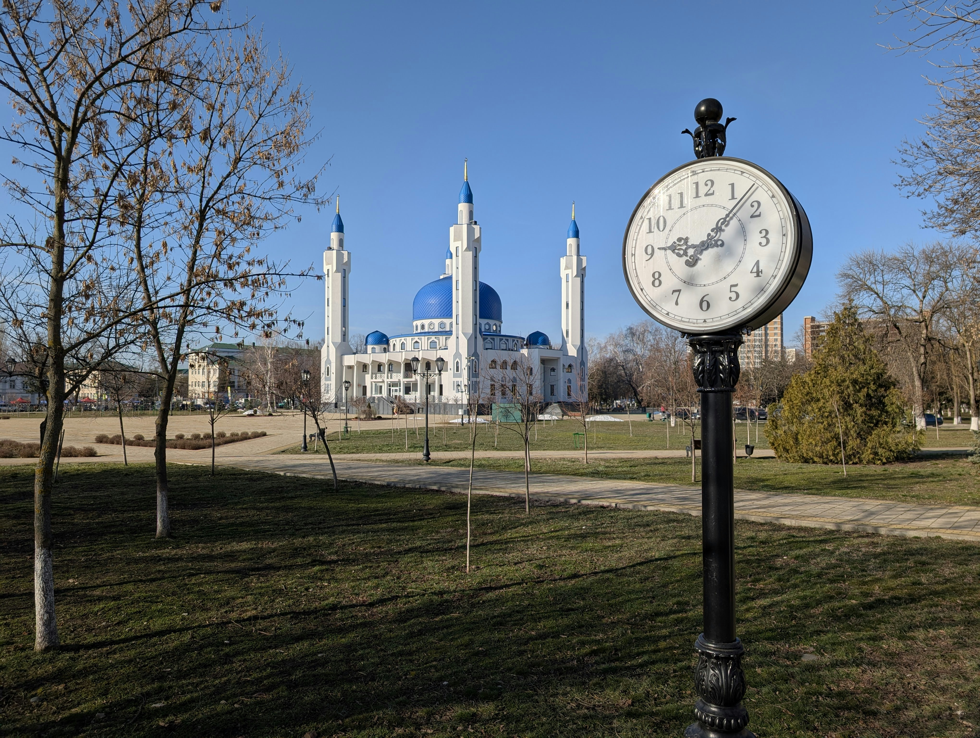 Ornate clock post with a backdrop of a blue-domed mosque under a clear sky.