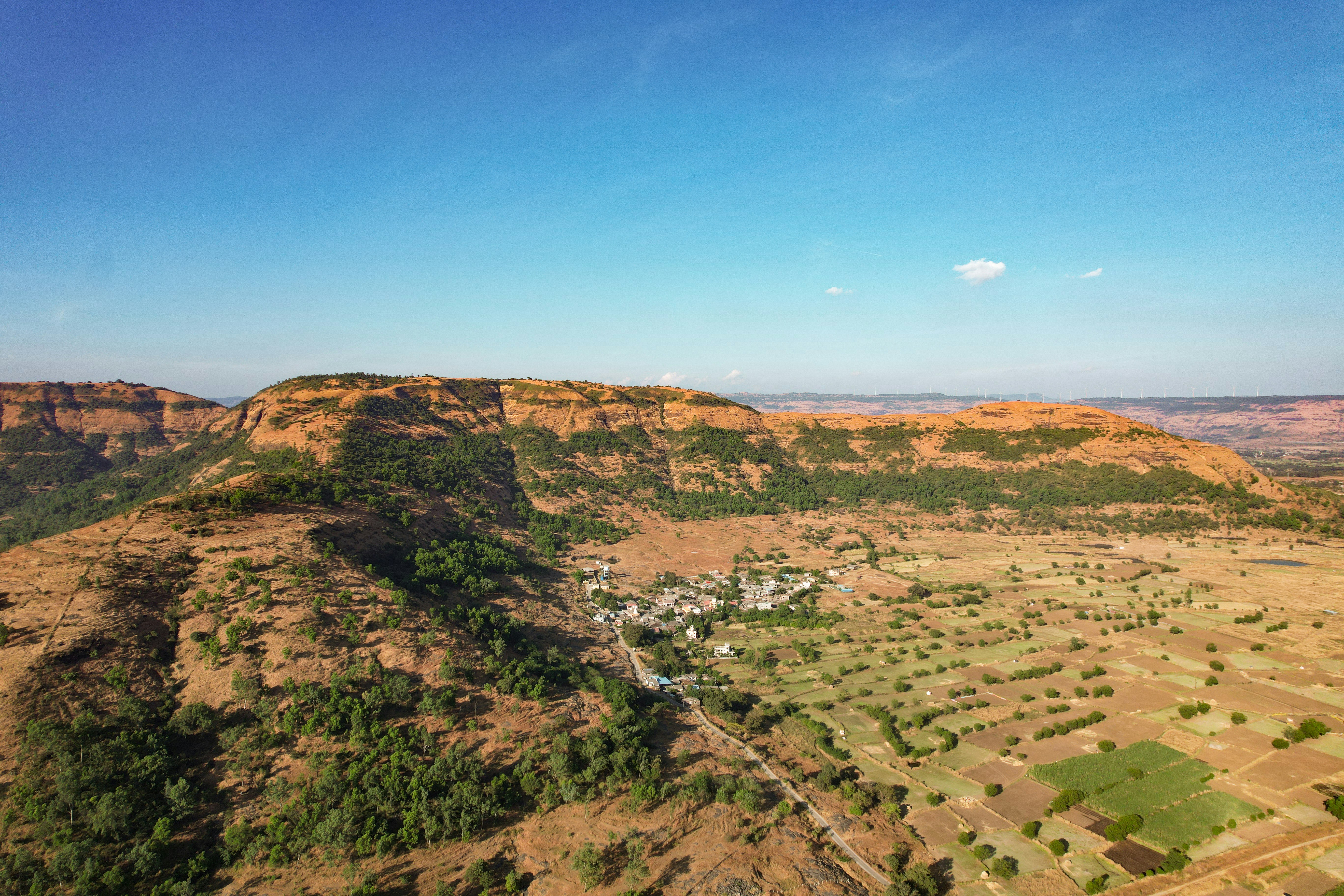 Expansive rural landscape with terraced fields and a small village nestled between sunlit hills under a clear blue sky.