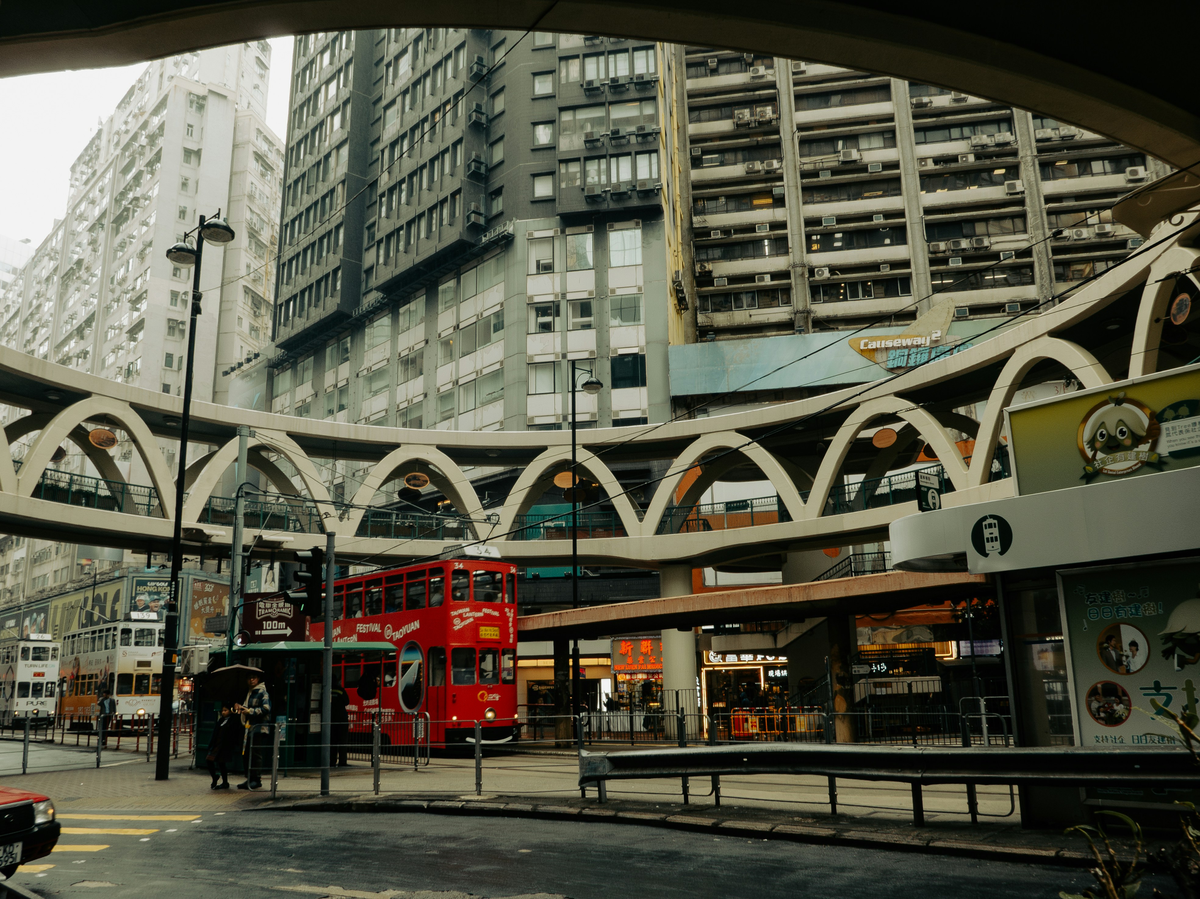 Red double-decker tram under circular pedestrian bridge in Hong Kong.