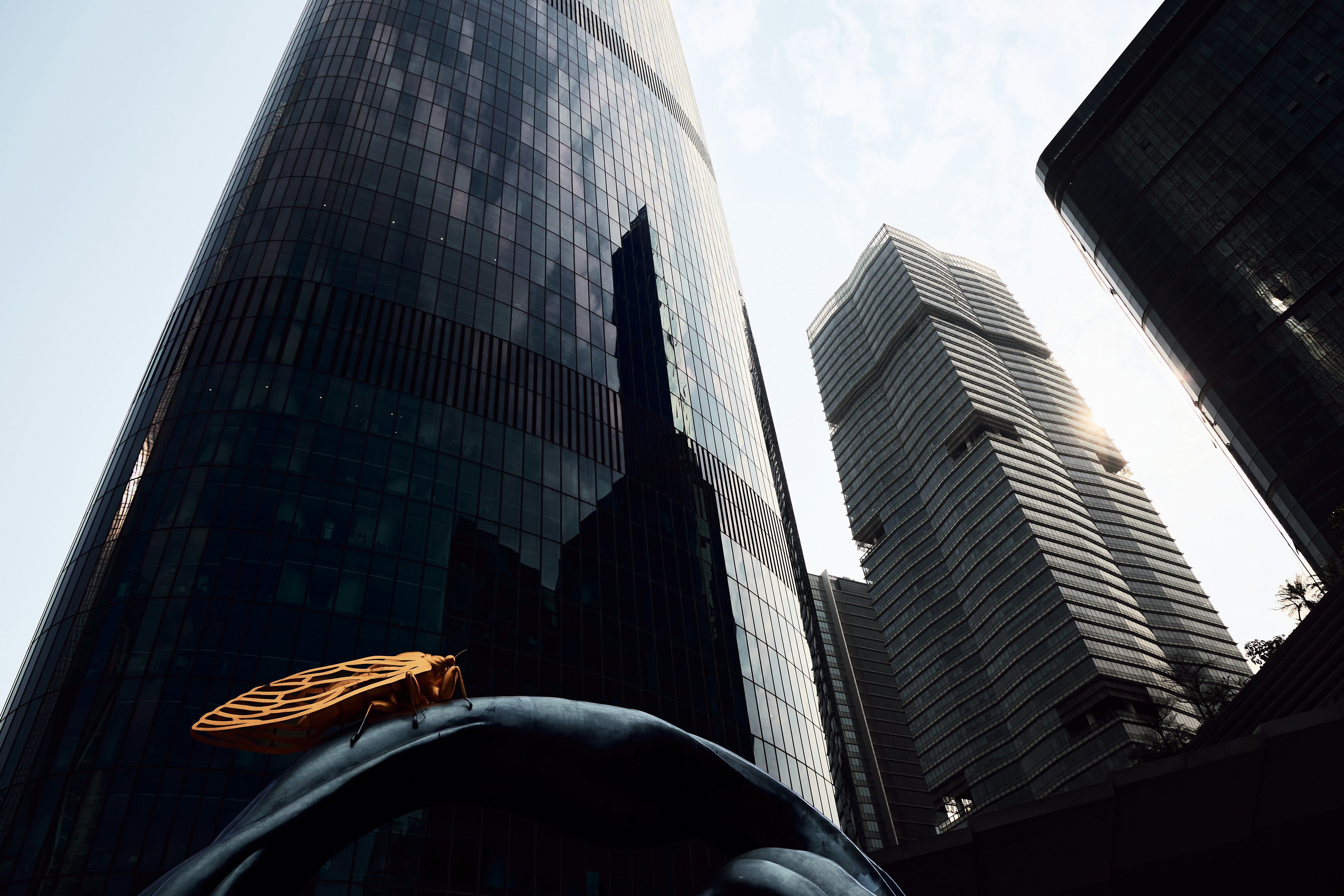 Large bug sculpture on a modern statue with towering skyscrapers in the background.