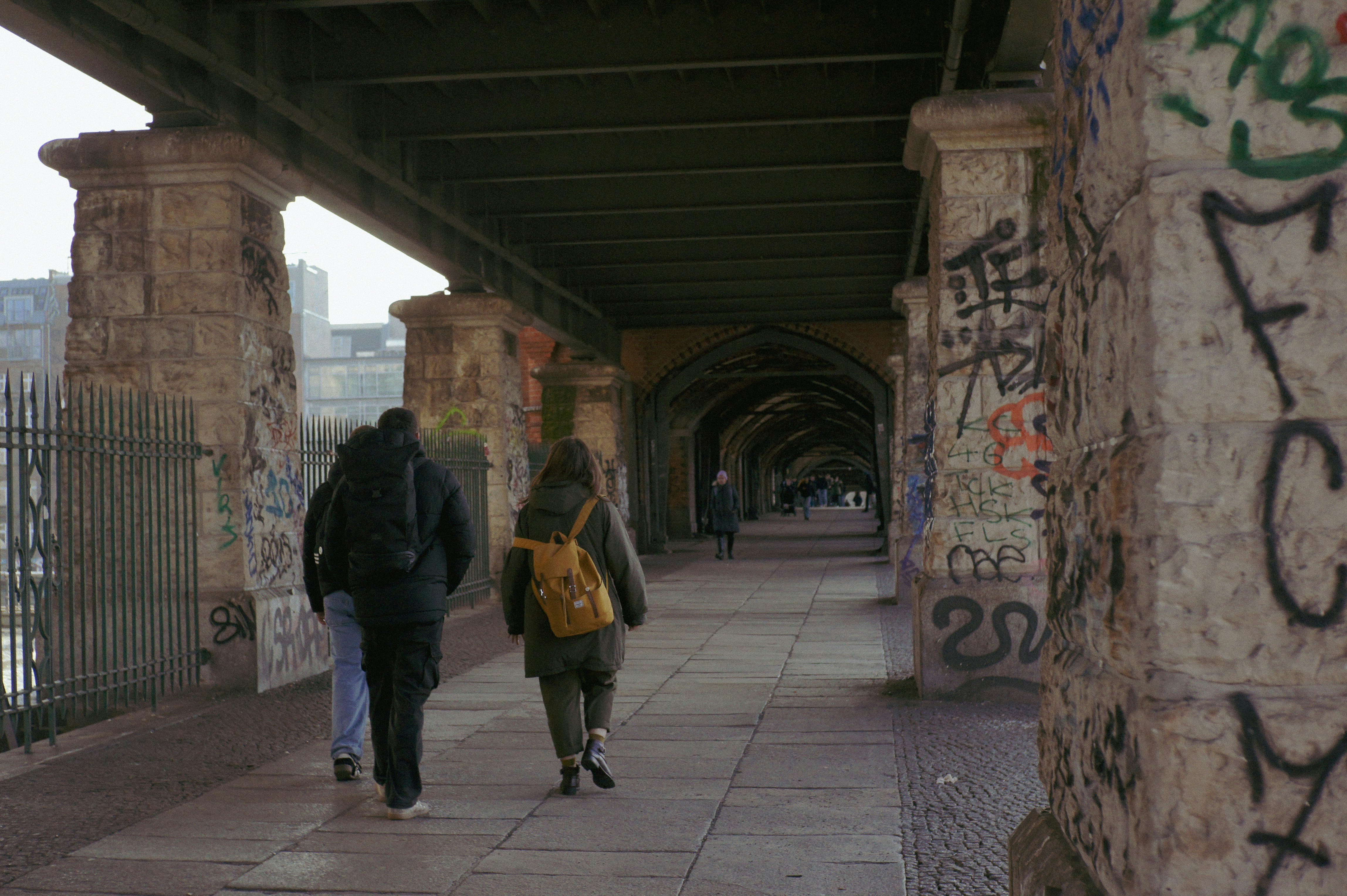 People walk under a bridge with graffiti. photo – Free People Image on ...