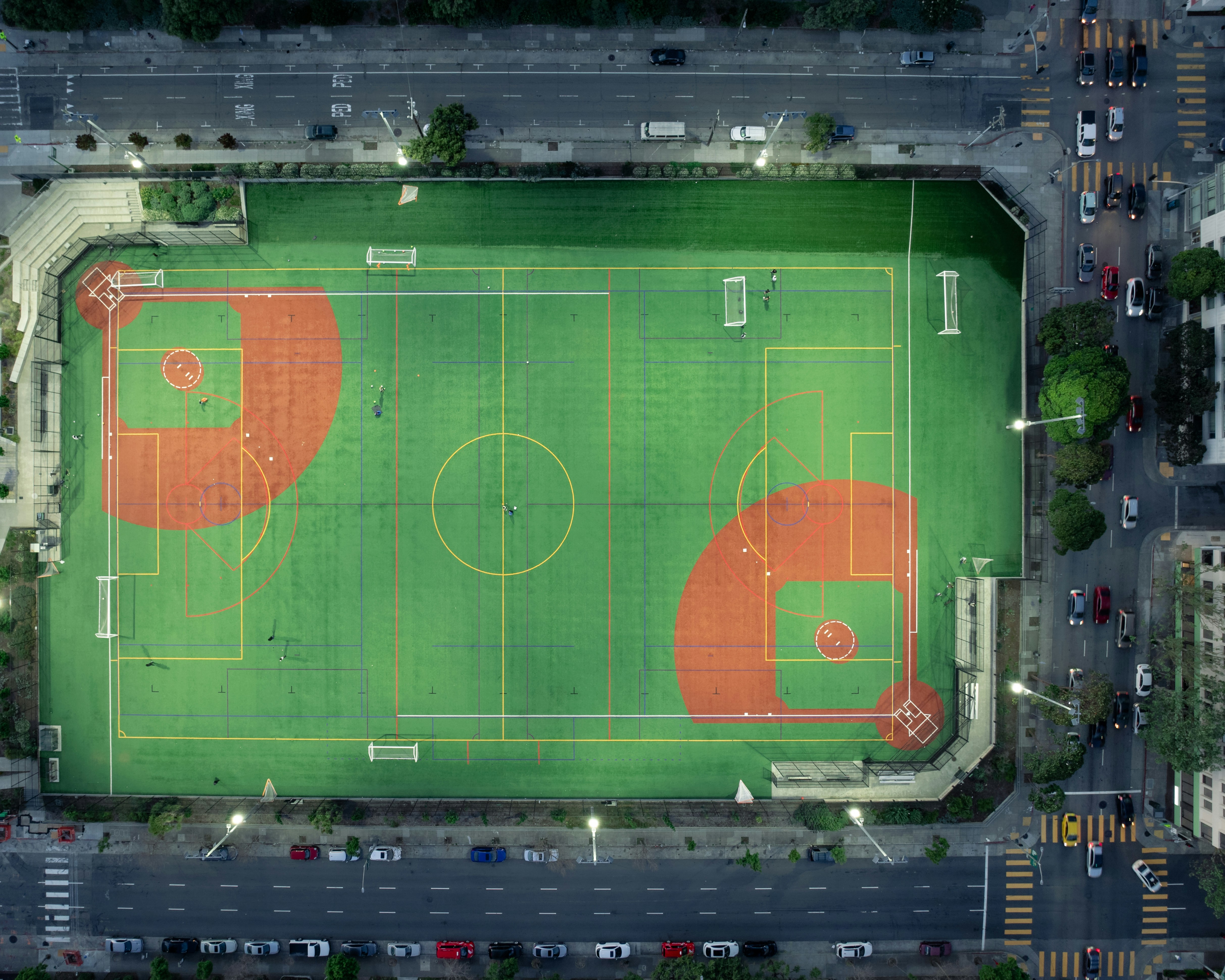 Aerial view of a vibrant multi-sport field bordered by city streets at dusk.