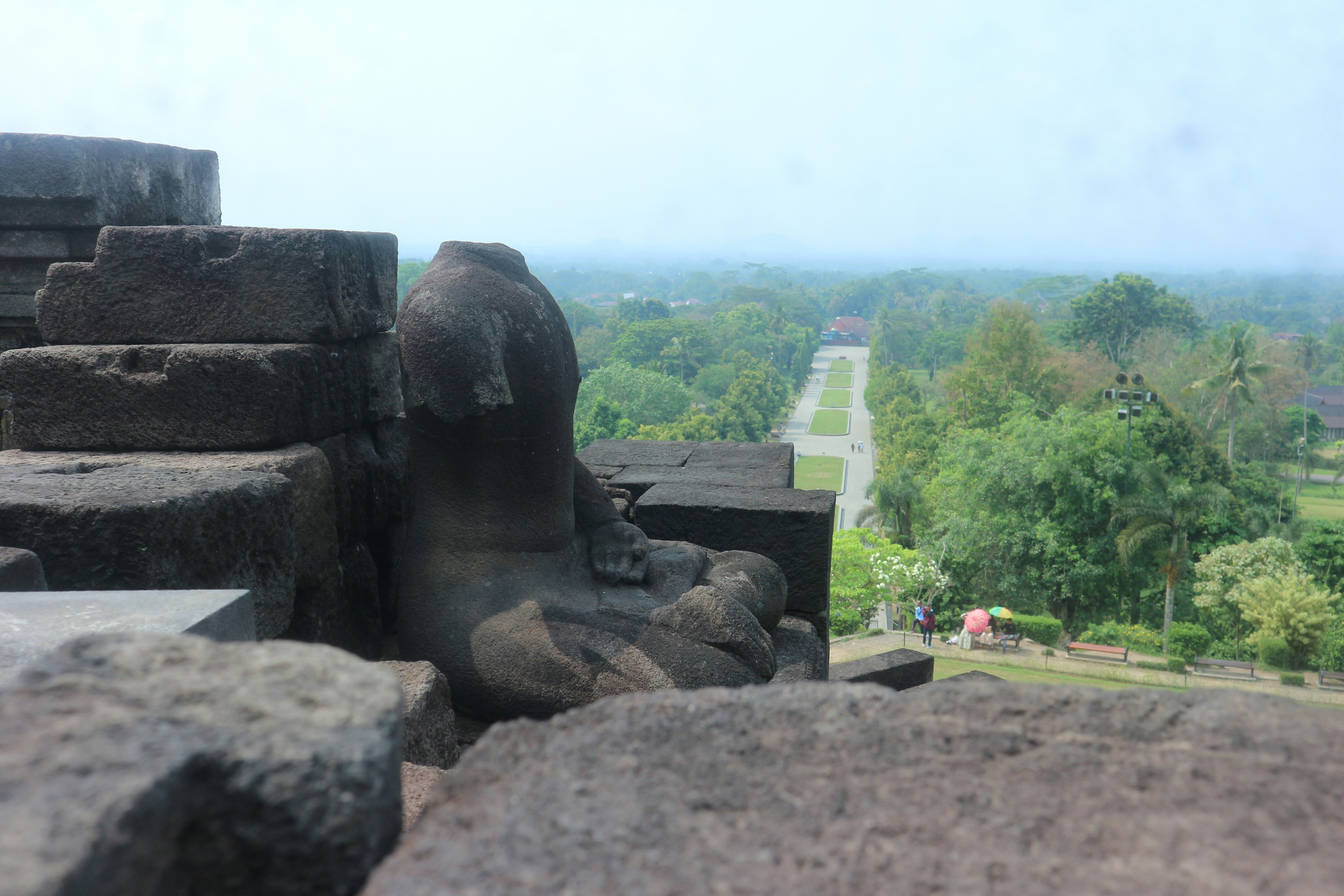 Stone statue gazes over a lush landscape with a distant road.
