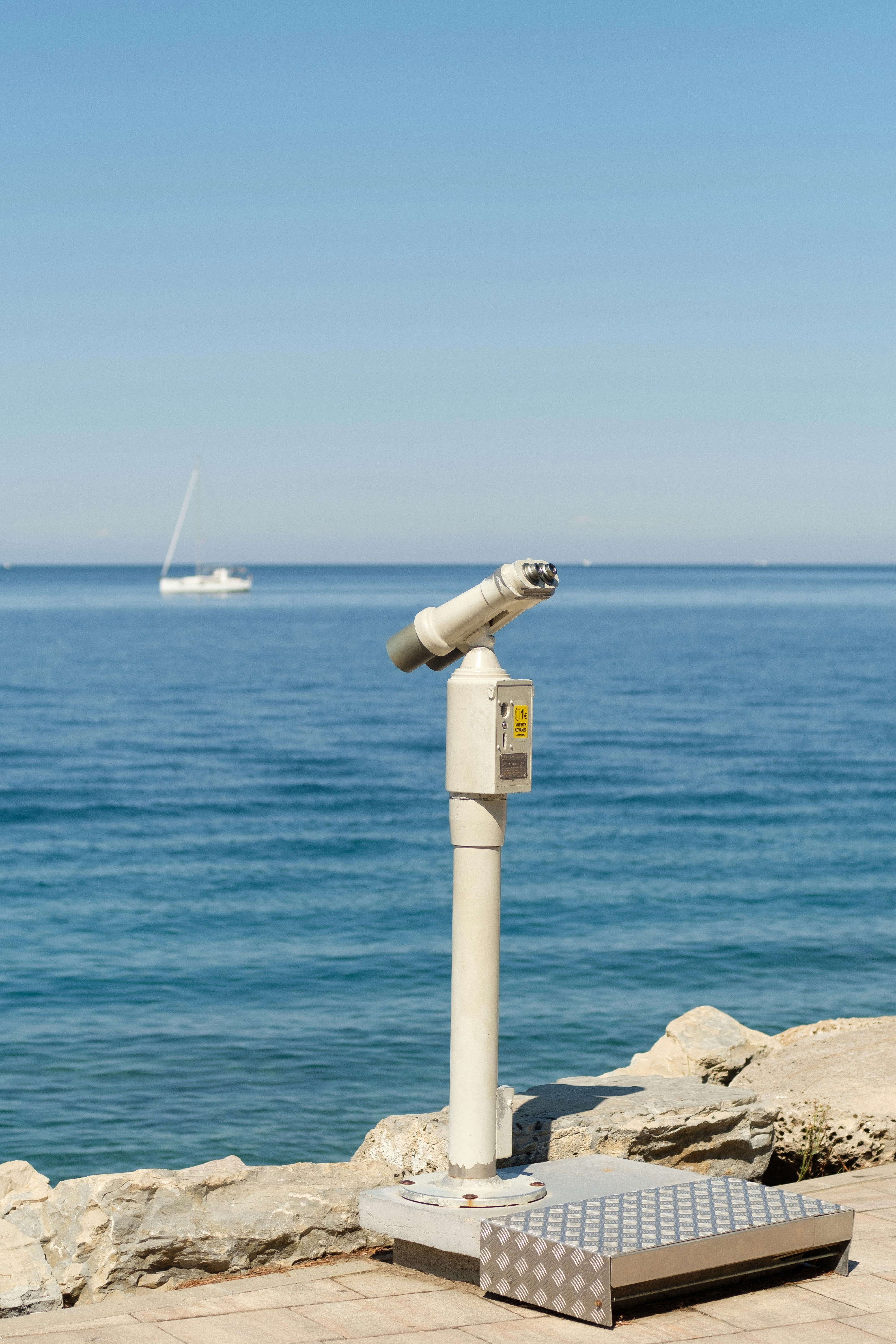 Harbor Optics: A lone telescope framing a tranquil sea and distant sailboat