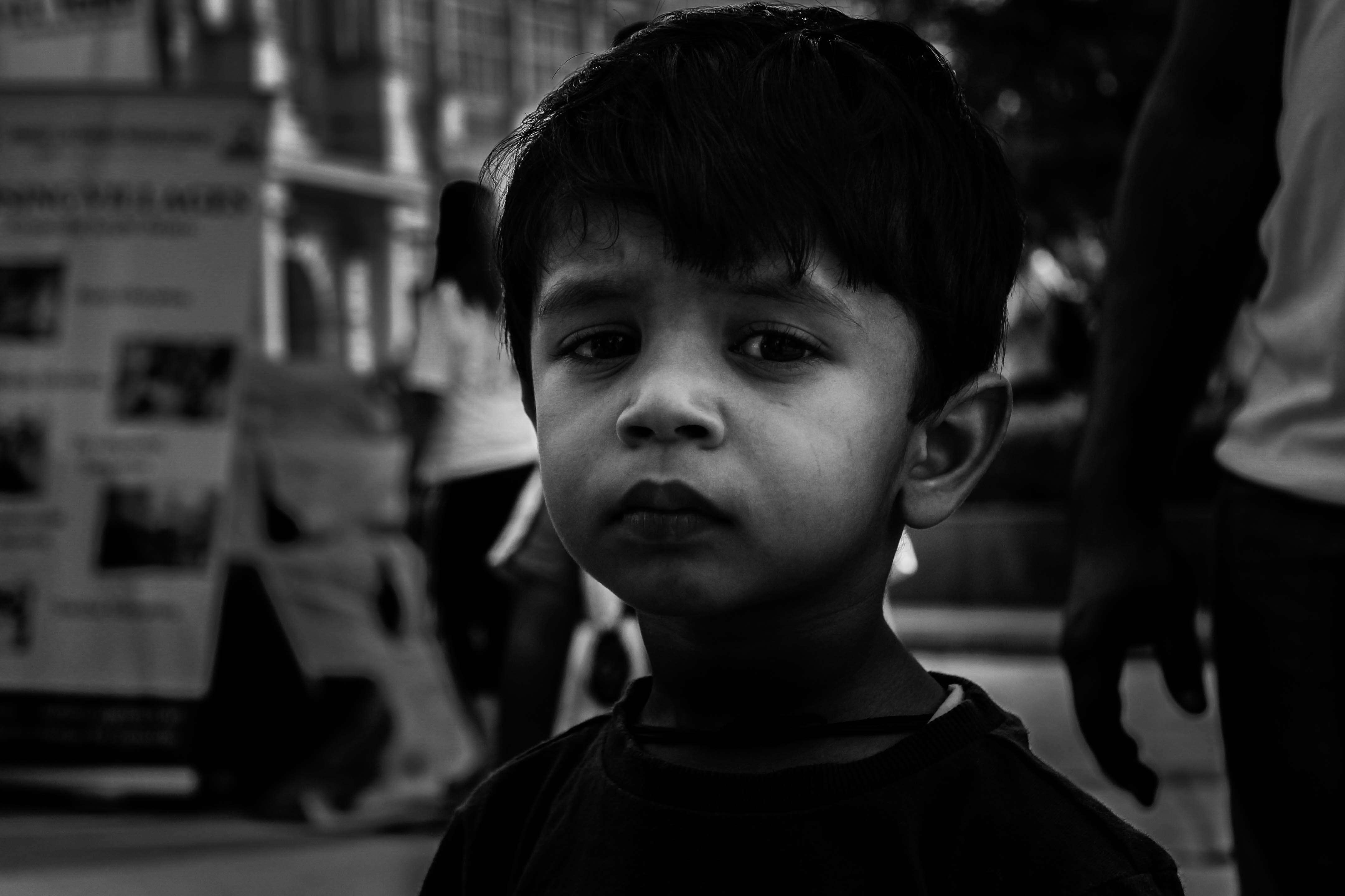 A child with a thoughtful expression stands in focus against a blurred urban backdrop.