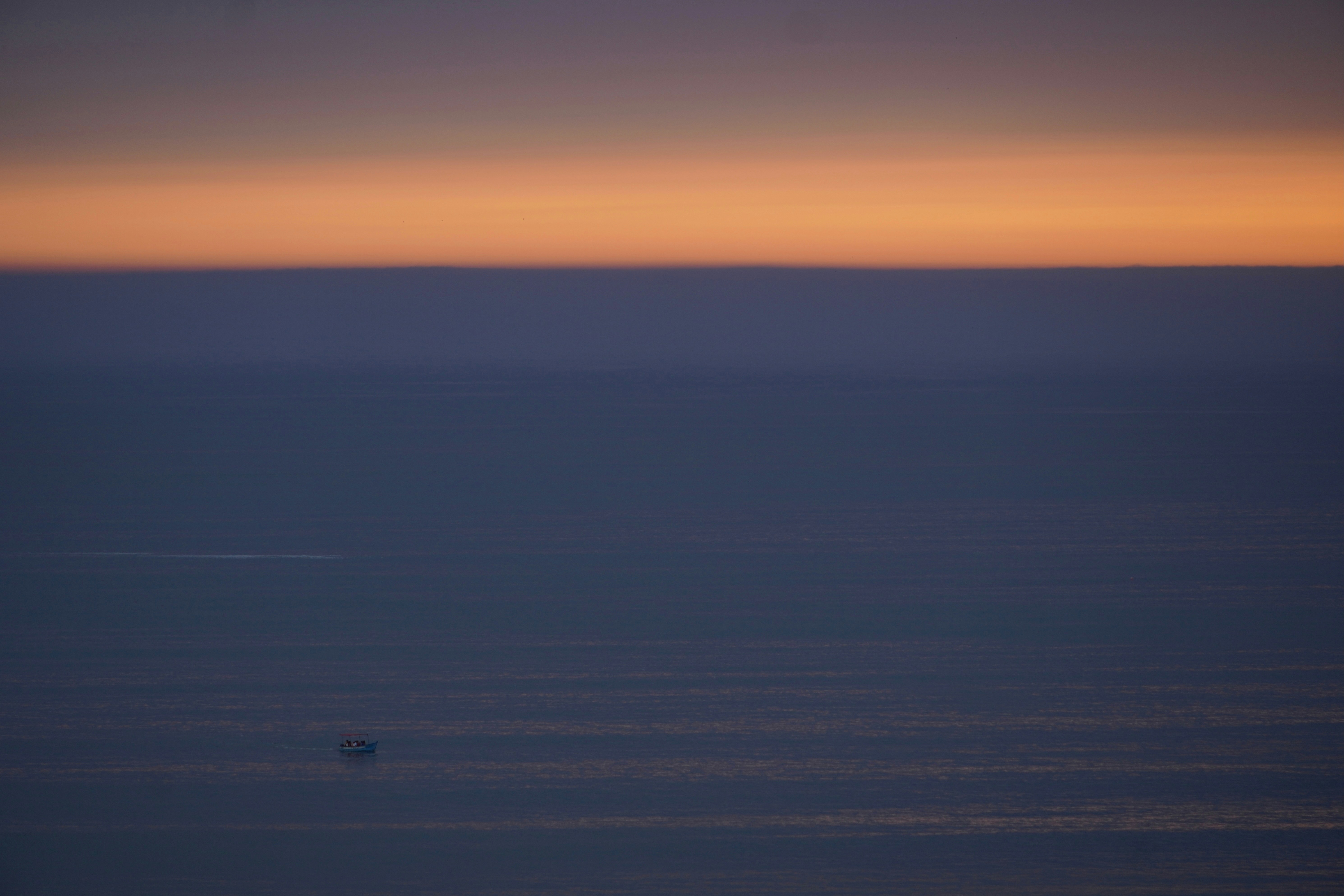 Lone boat floating on calm ocean under a gradient sunset sky.